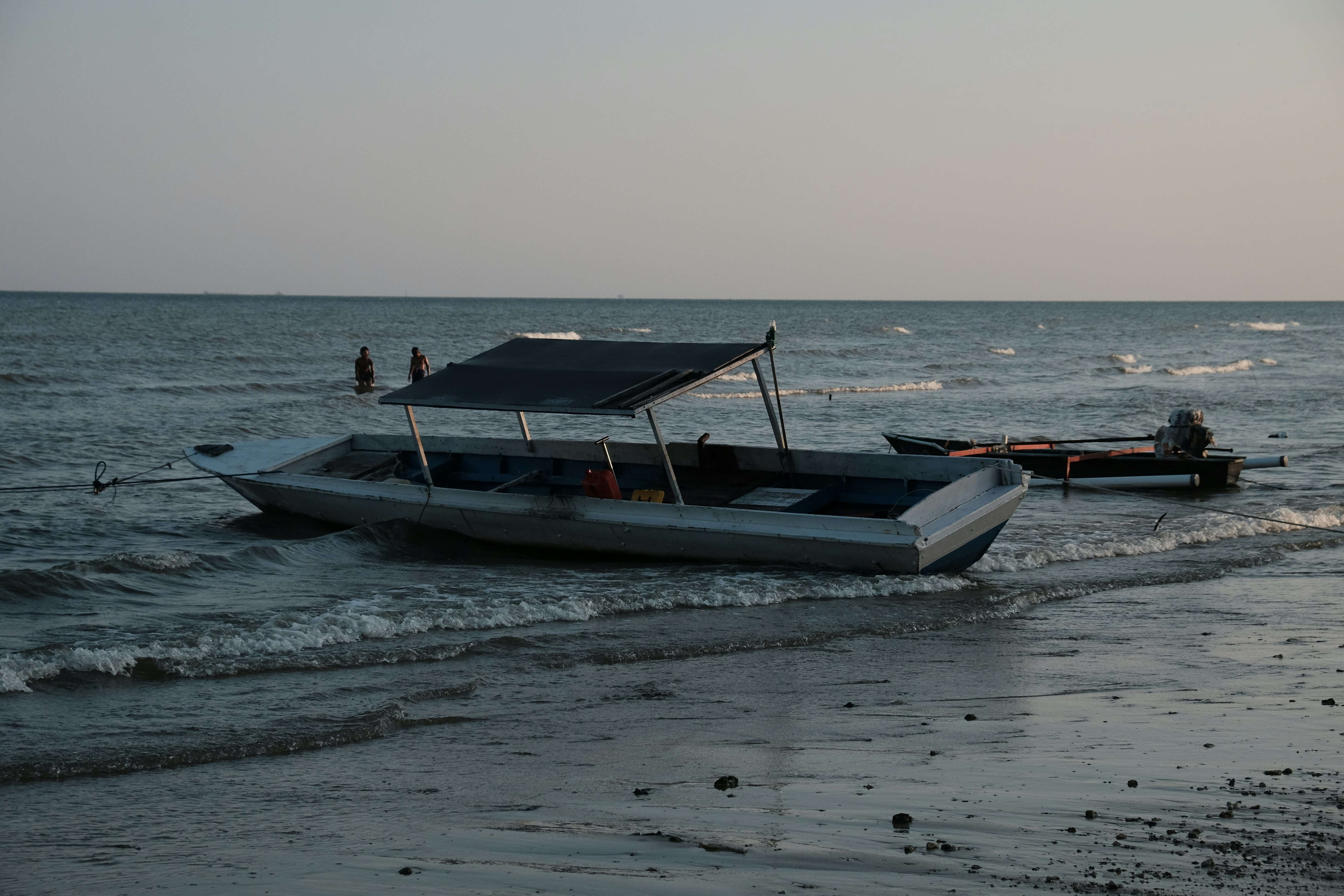 Boats rest near the shoreline as gentle waves wash onto a quiet beach at dusk.