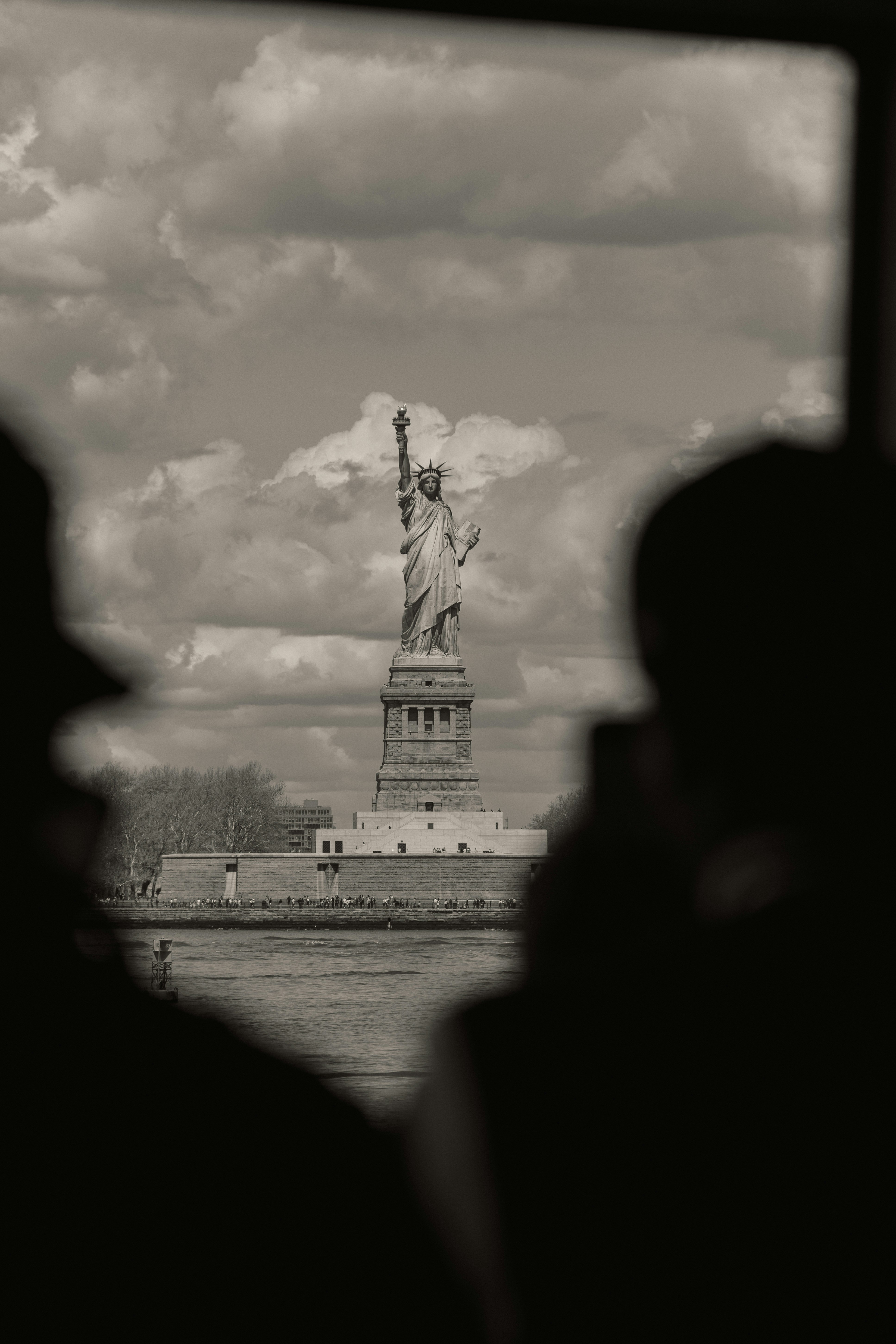 Statue of Liberty framed by silhouettes at riverfront viewing point