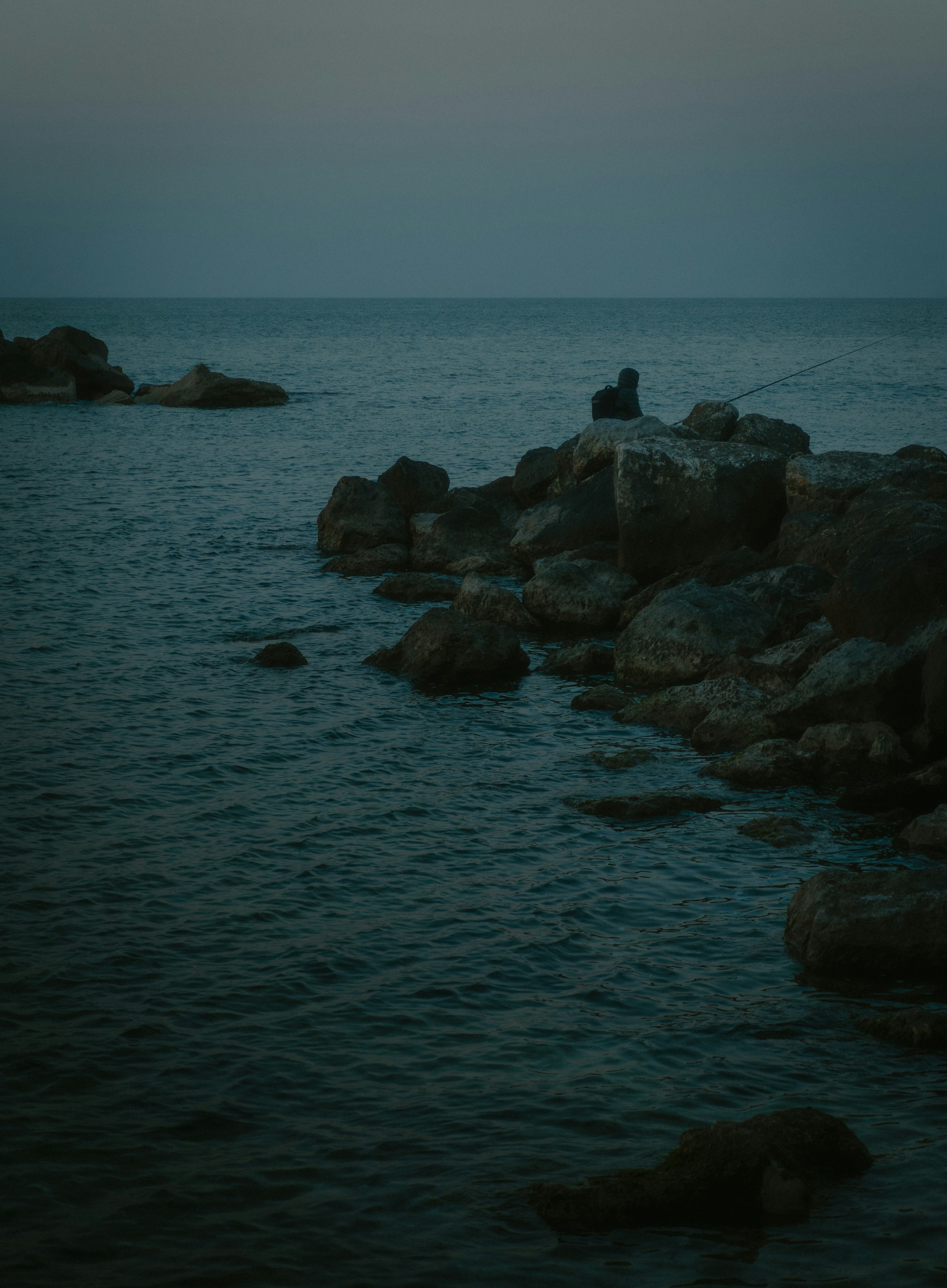 Rugged Breakwater: A Lone Fisherman Beneath A Quiet Horizon