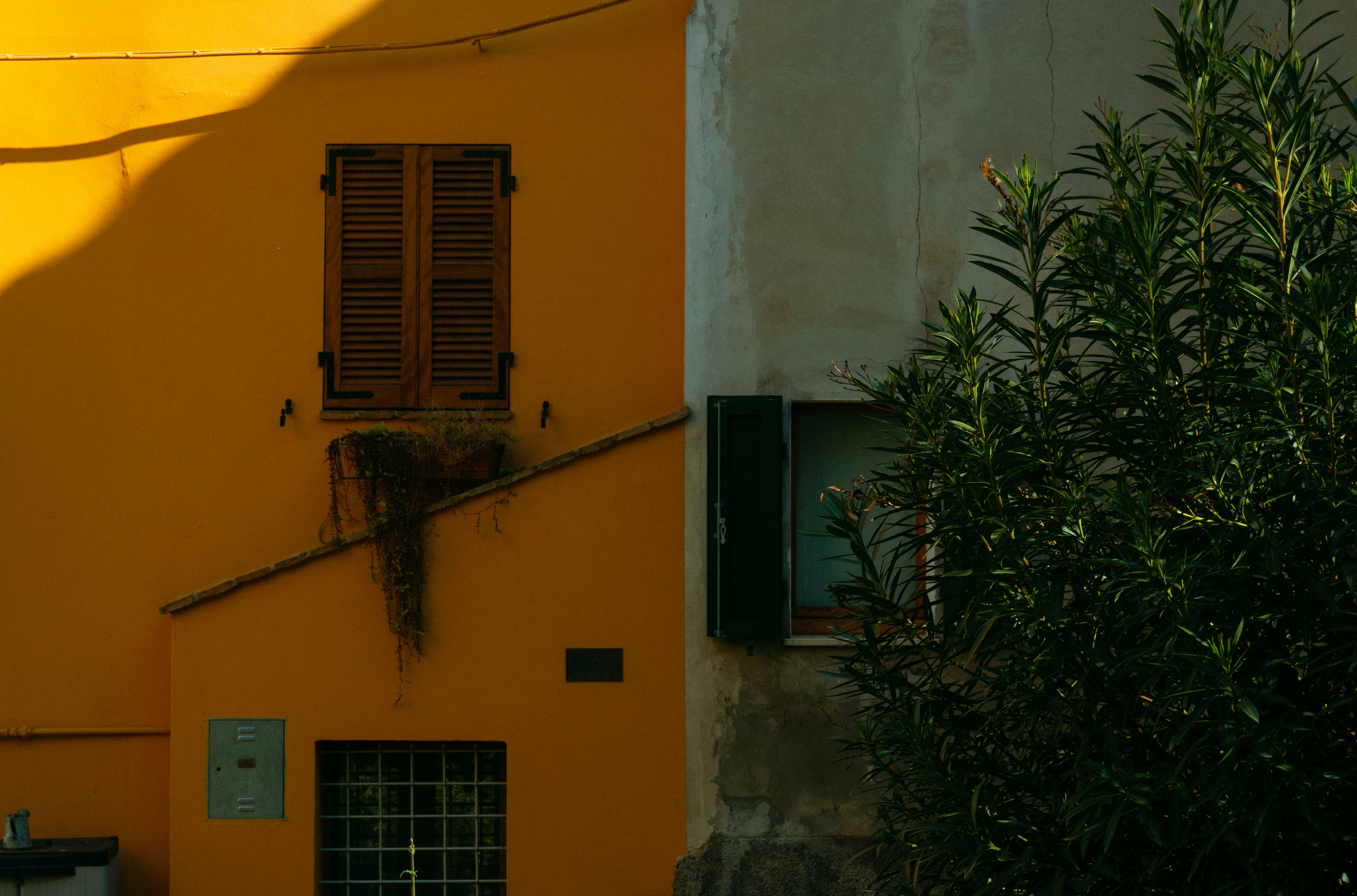 Sunlit Yellow Facade with Worn Window and Shadowed Nook