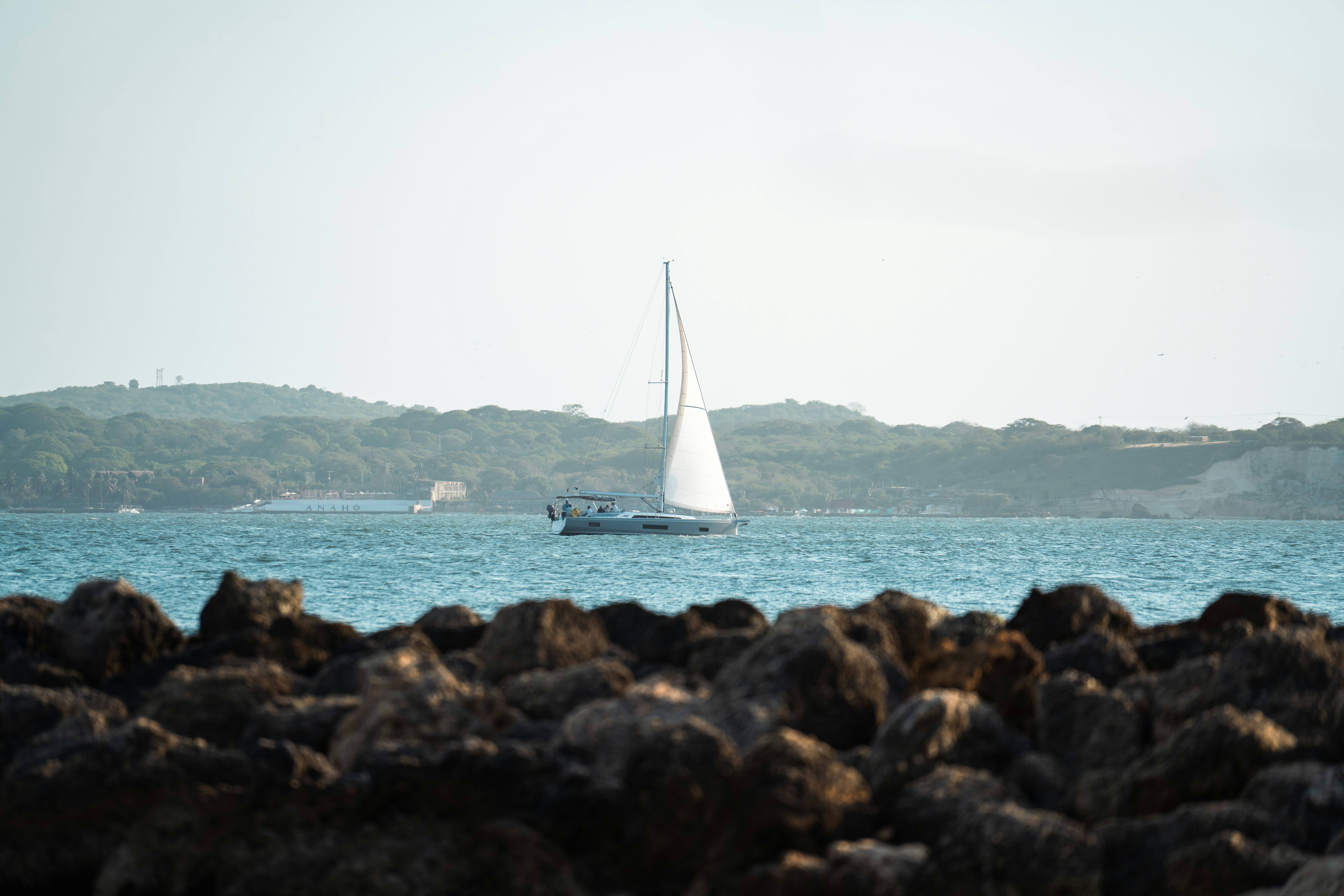 Sailboat Piercing a Quiet Sea as Rugged Foreshore Watches