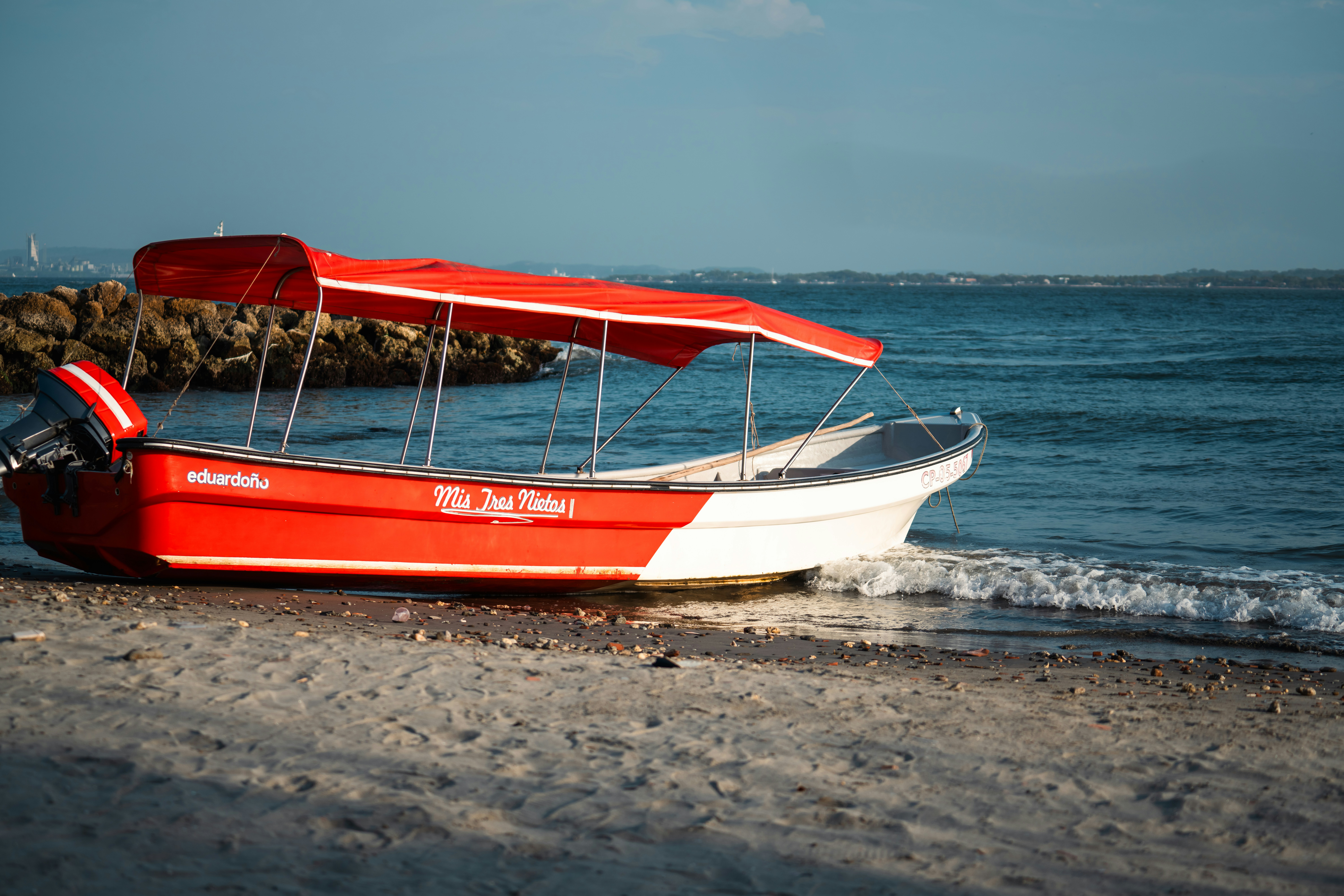 Red lifeline on the shore: a boat resting at the sunlit surf