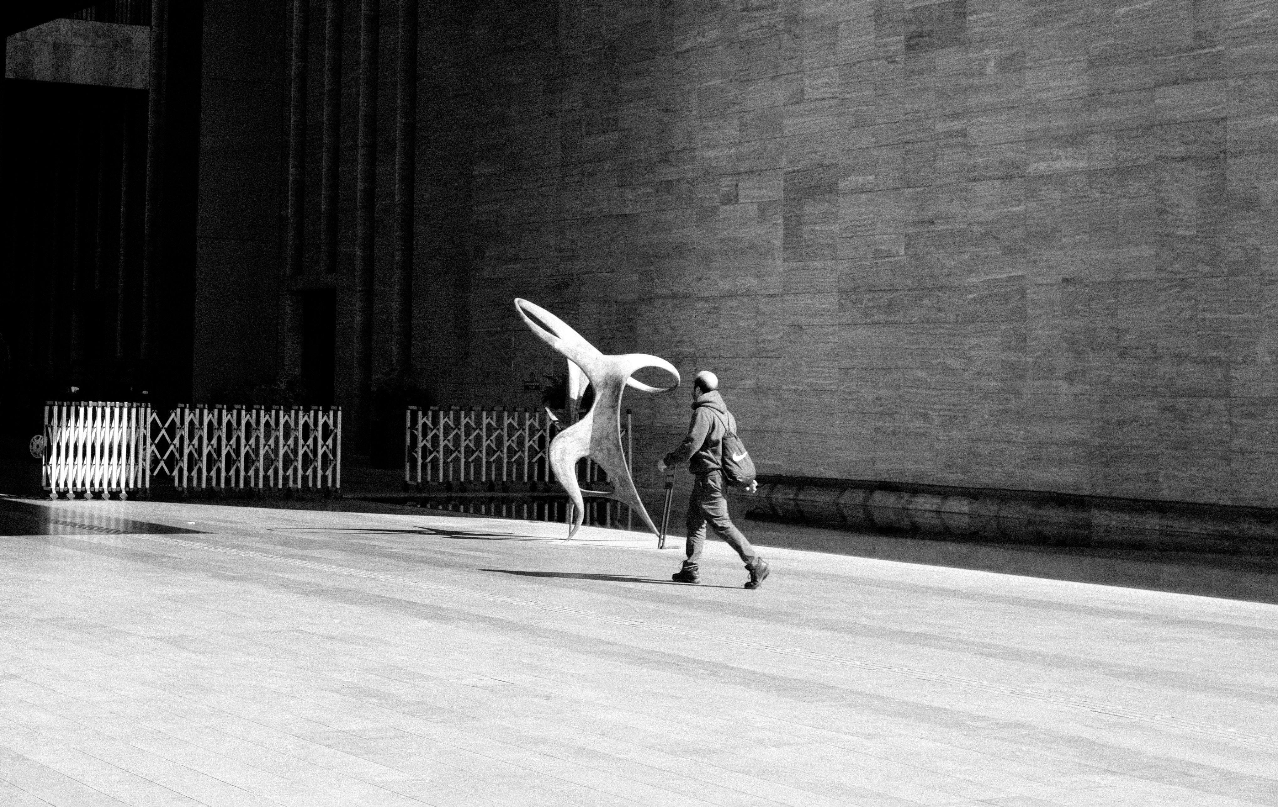 Solo ballet of a sculpture and a walker in a sunlit plaza