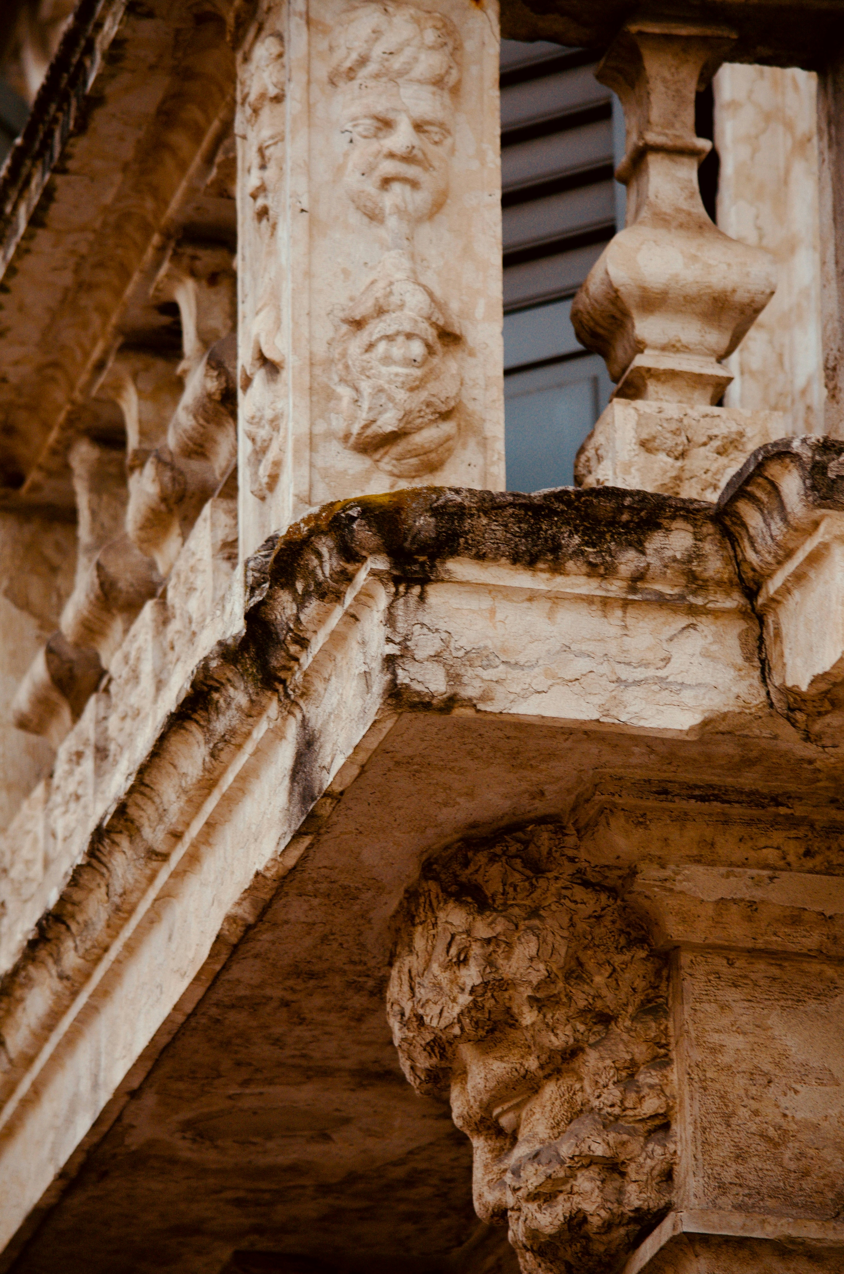 Stone Carved Balcony Faces: A Weathered Facade in Sepia Tones