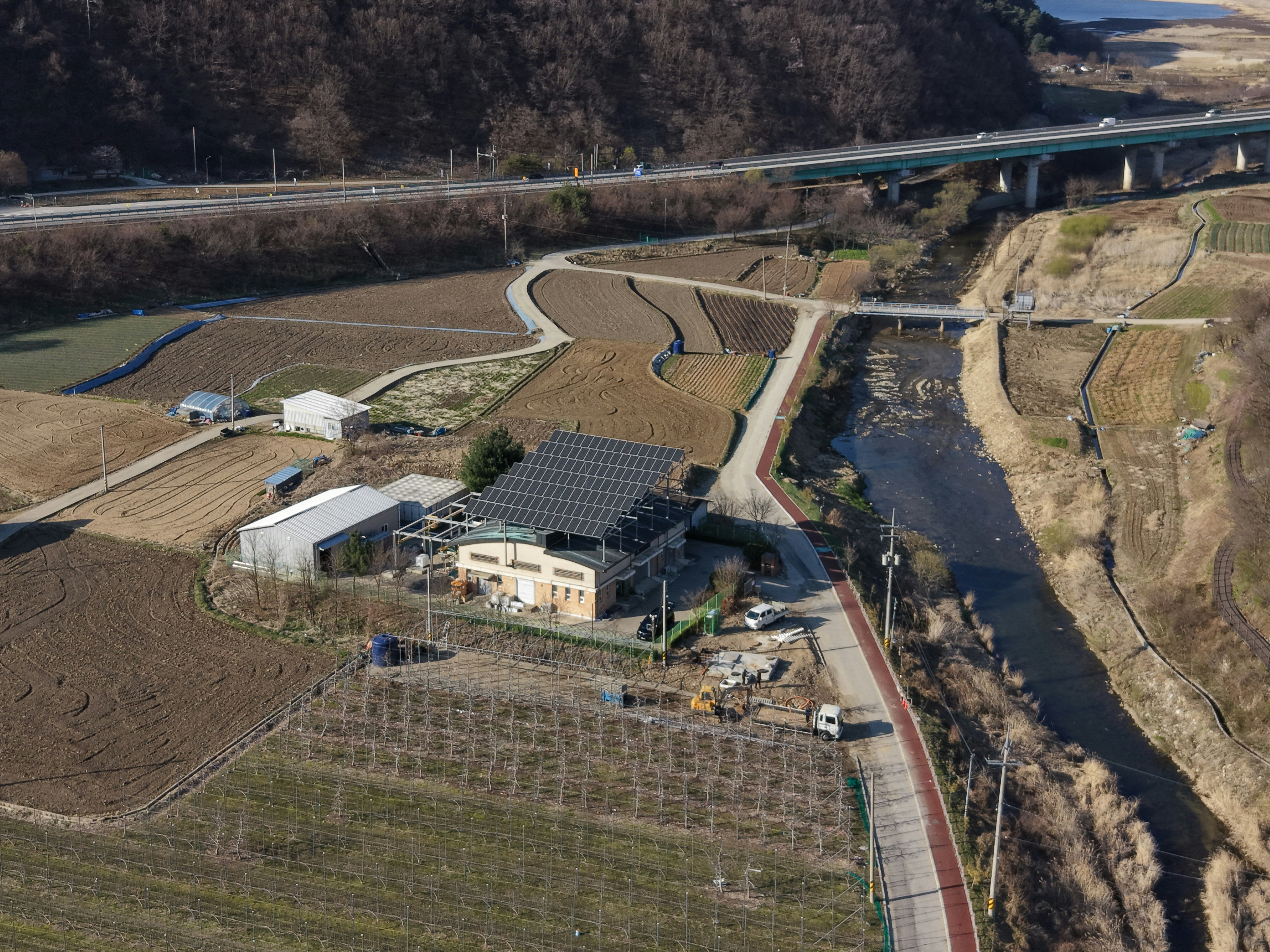 Riverside Farmstead Under an Approaching Bridge