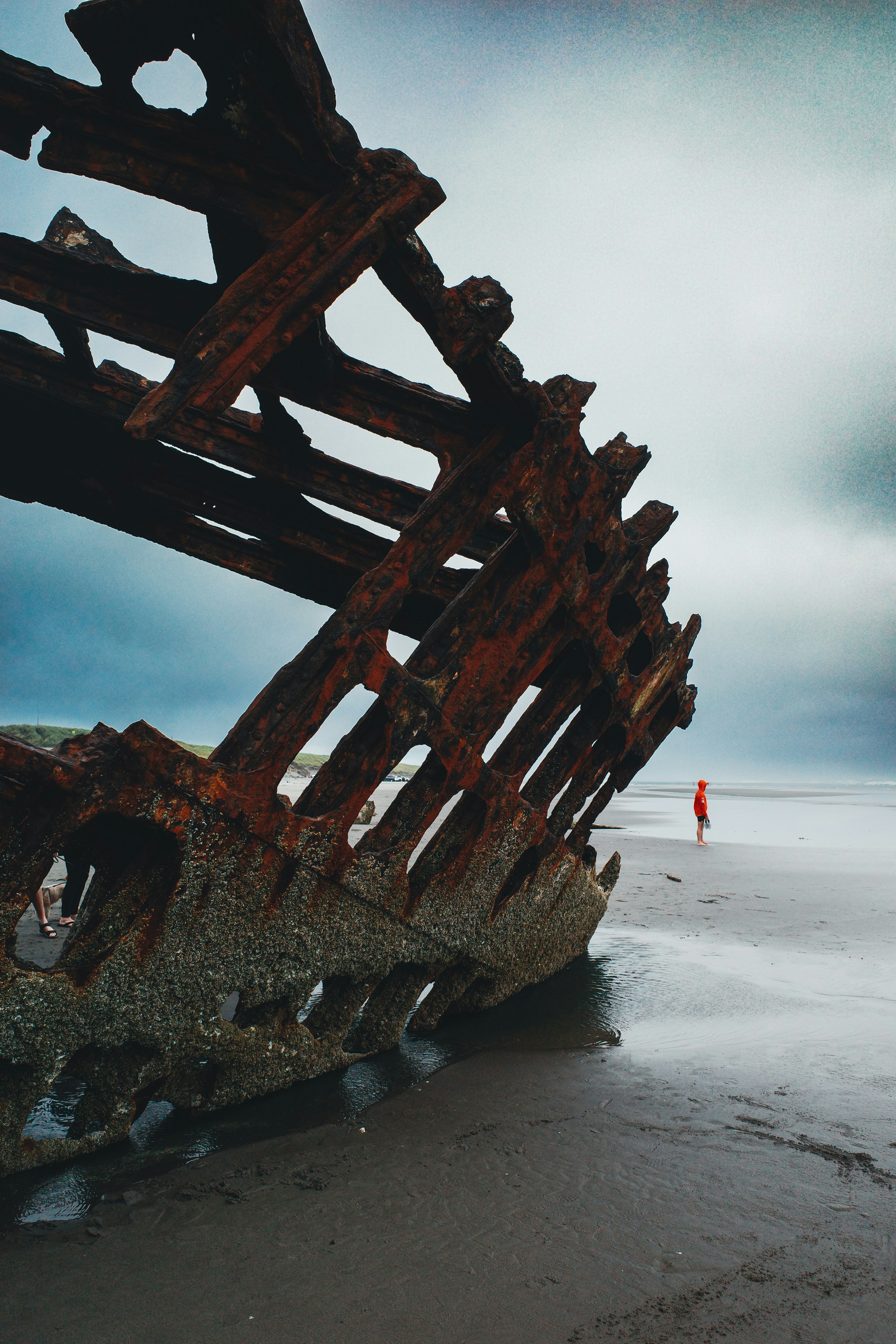 Rusty shipwreck hull on a sandy beach with person.