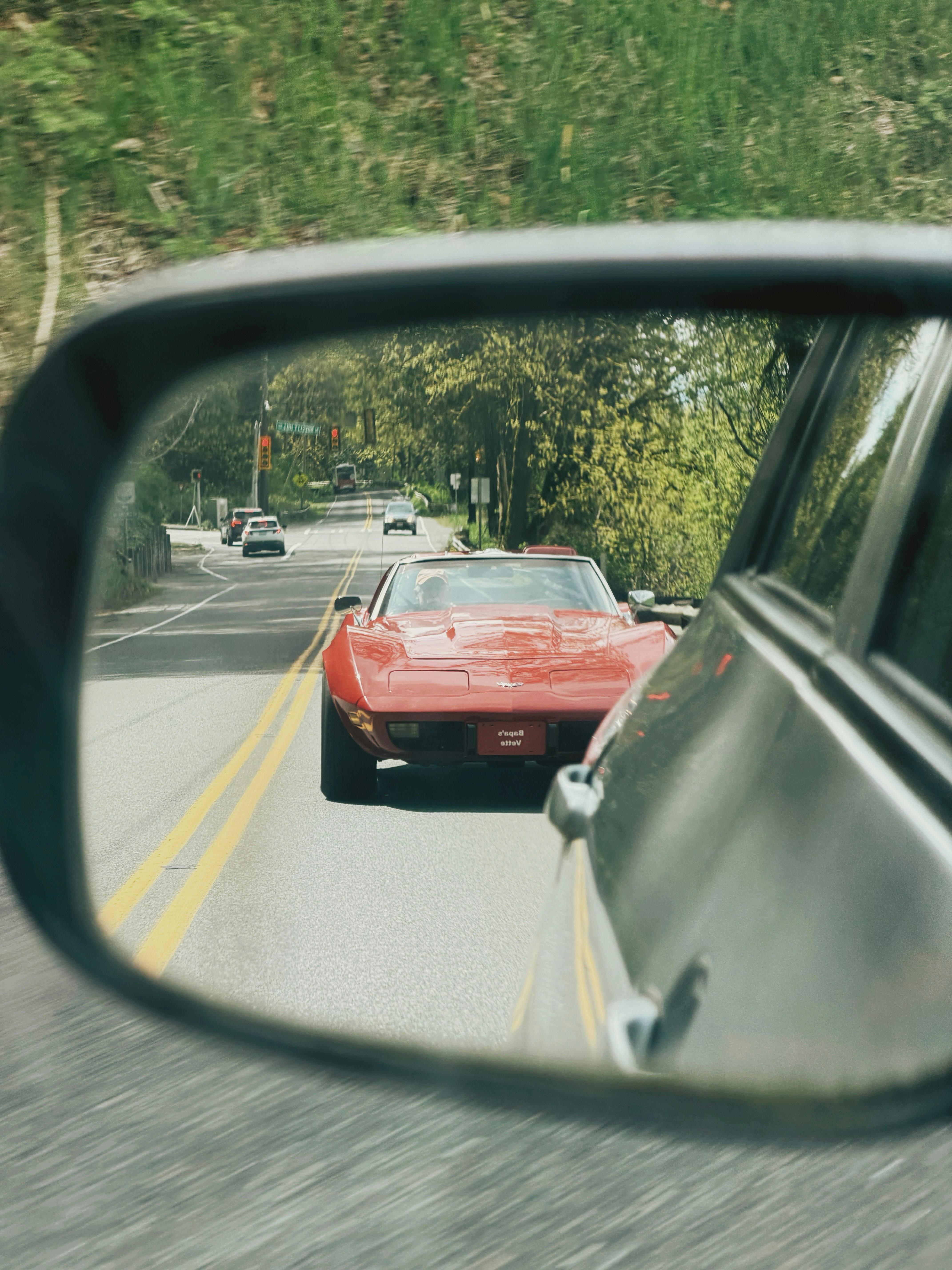 Rearview Rival: The Red Corvette in a Street-side Mirror