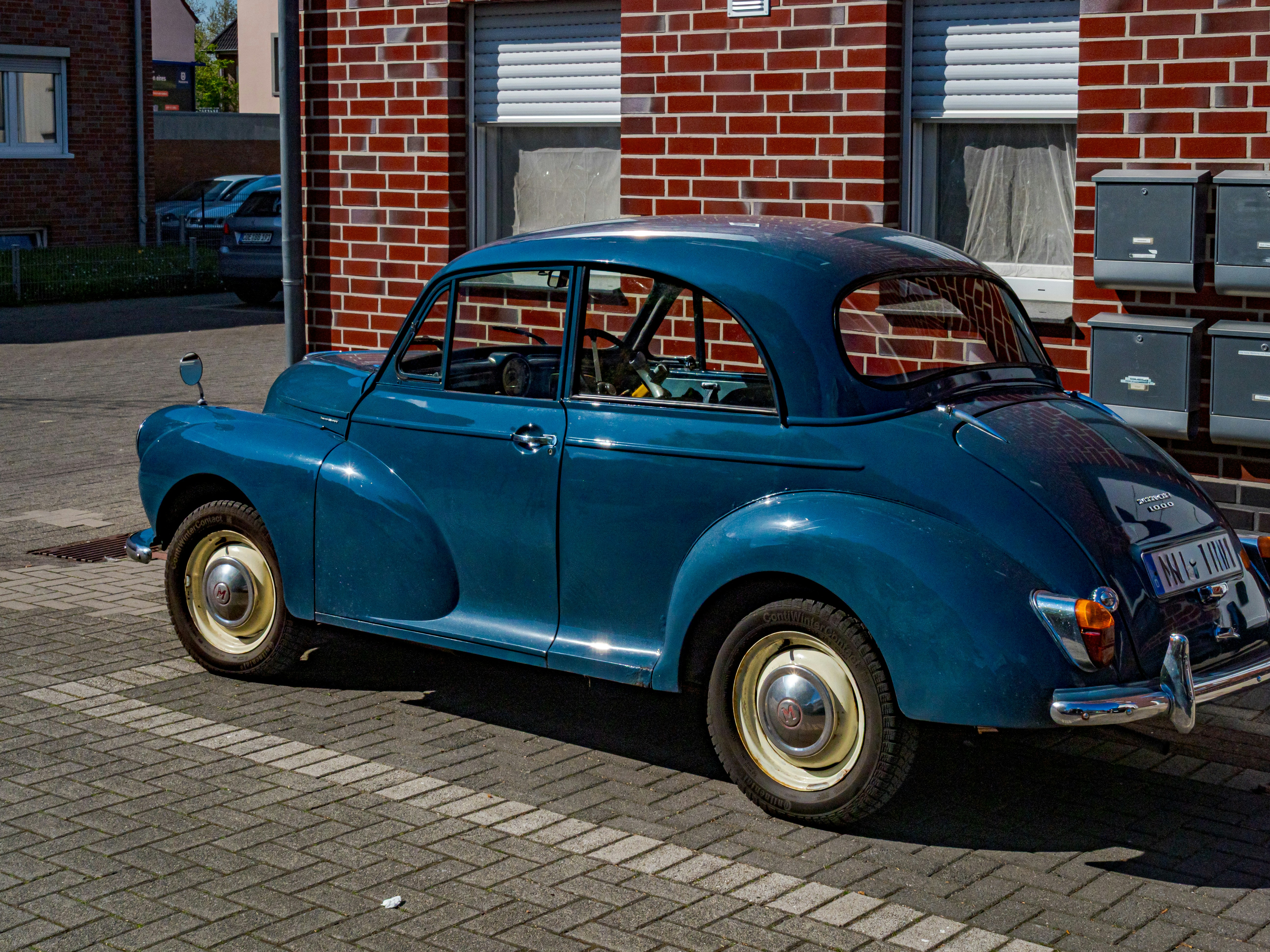 Blue vintage coupe under warm daylight by brick walls
