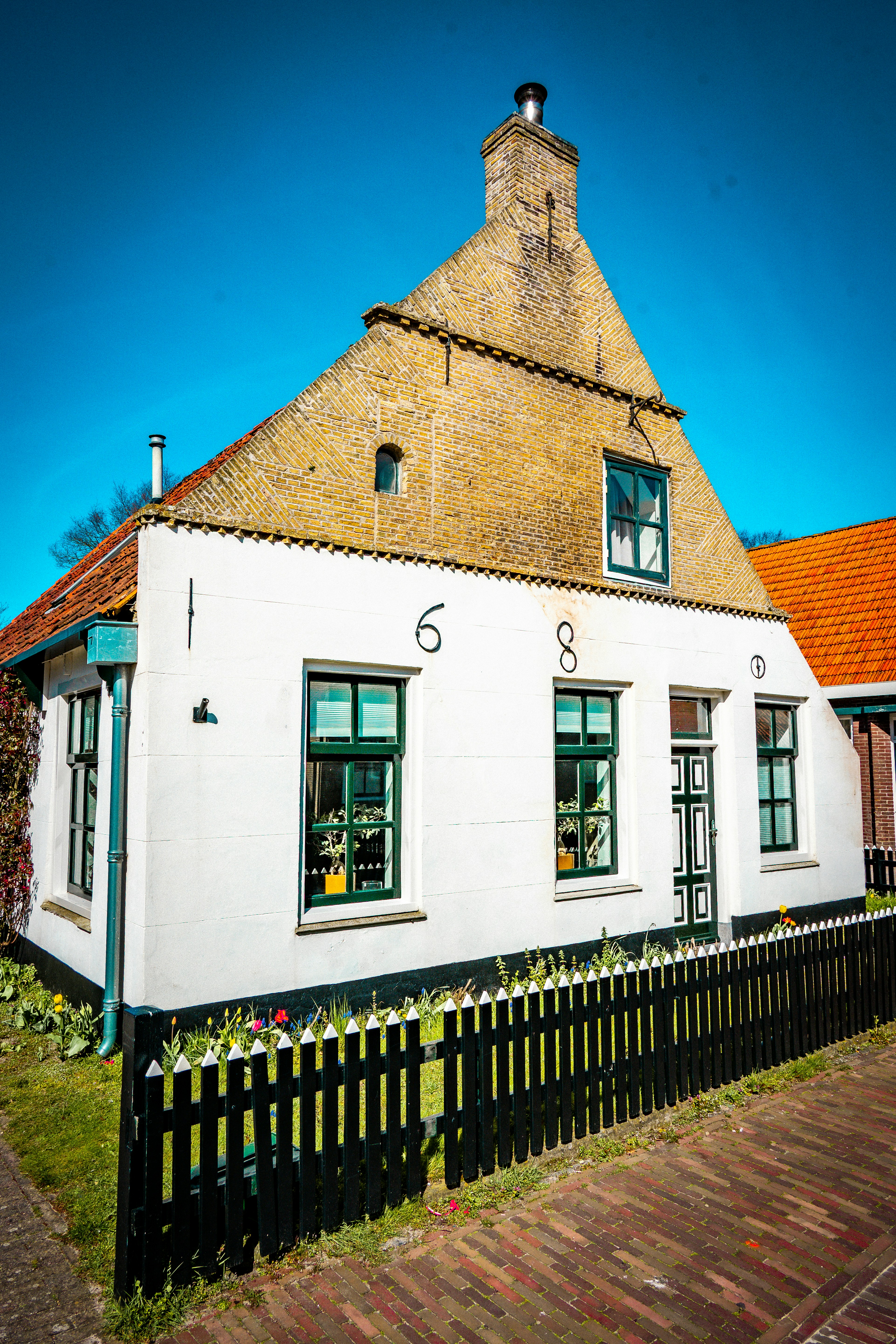 Charming brick-roofed cottage with white-washed façade and picket garden