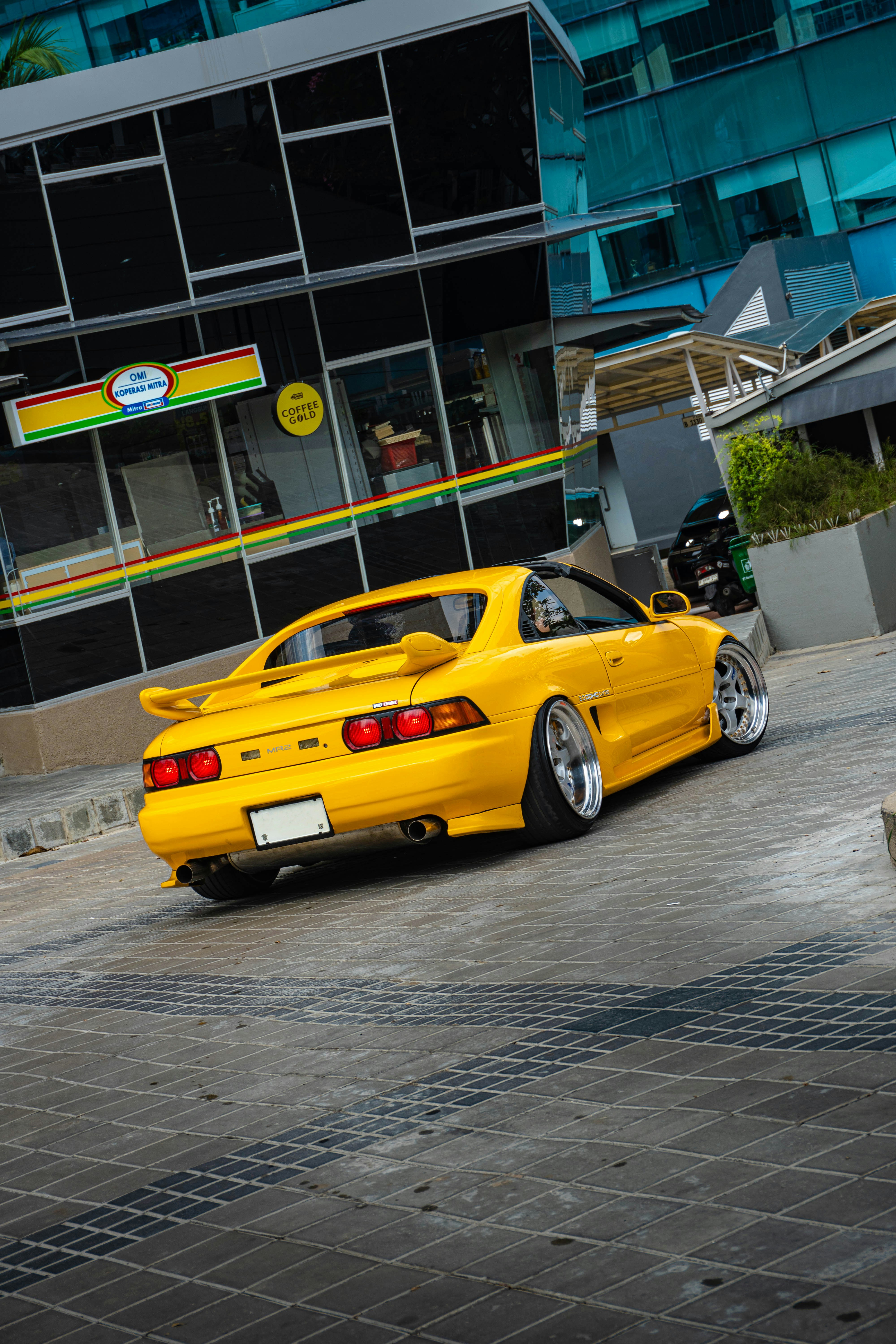 Sunlit GT: A Bold Yellow Dream Parked Before Modern Glass