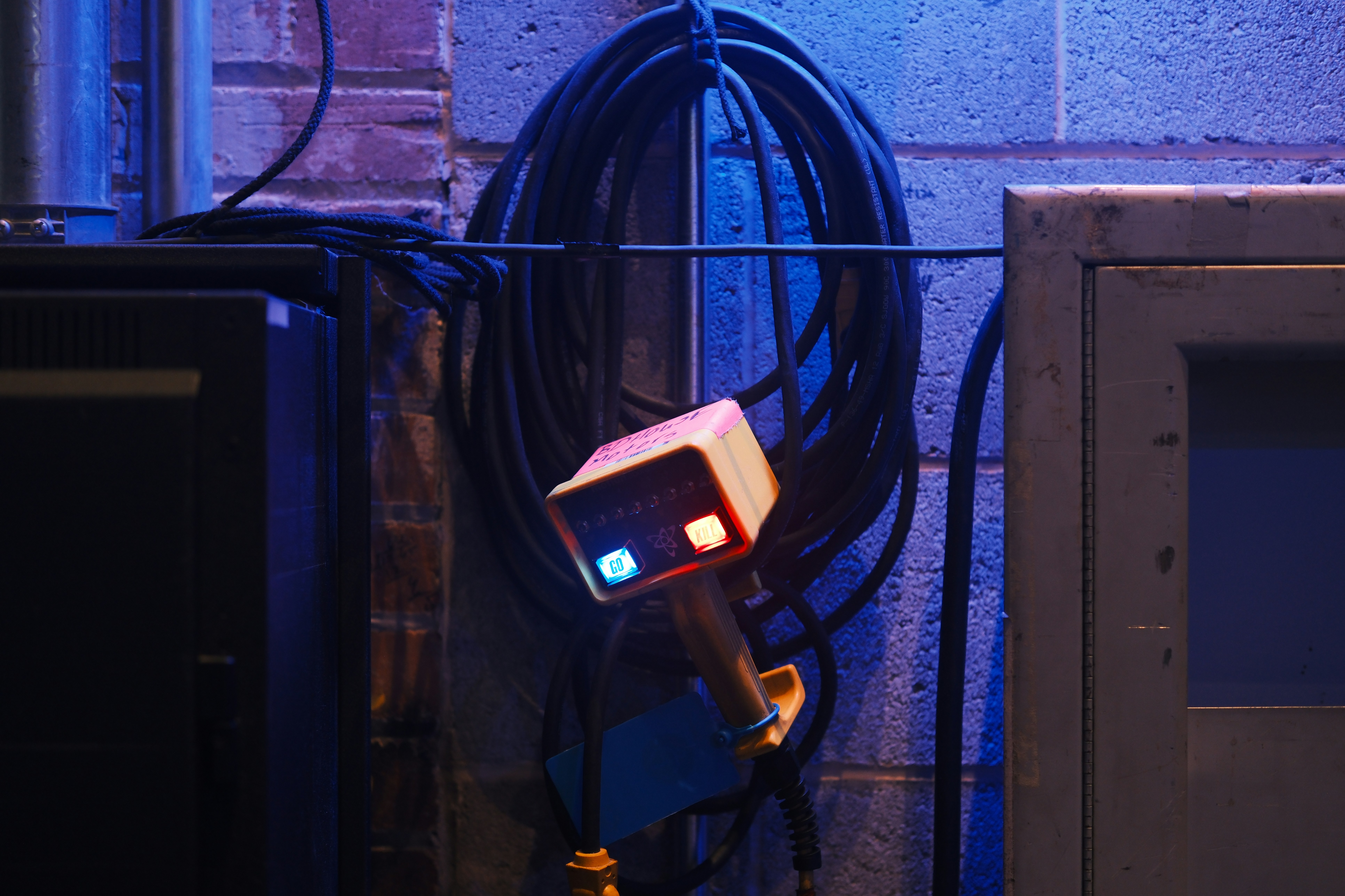 Neon-lit utility hub: a red-and-blue diagnostic tool suspended among cables