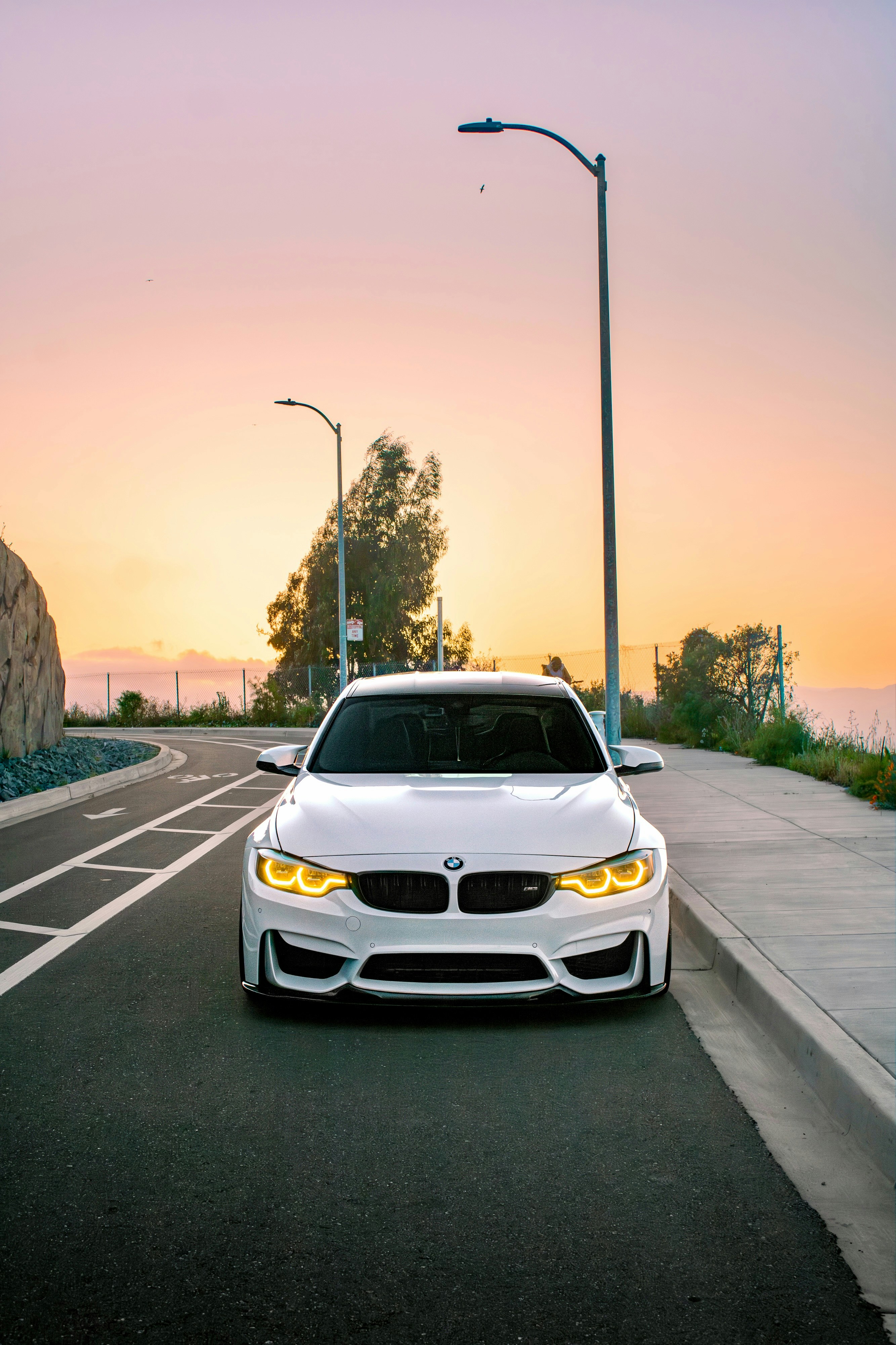 White BMW on an Avenueside at Sunset, with Glowing Headlights