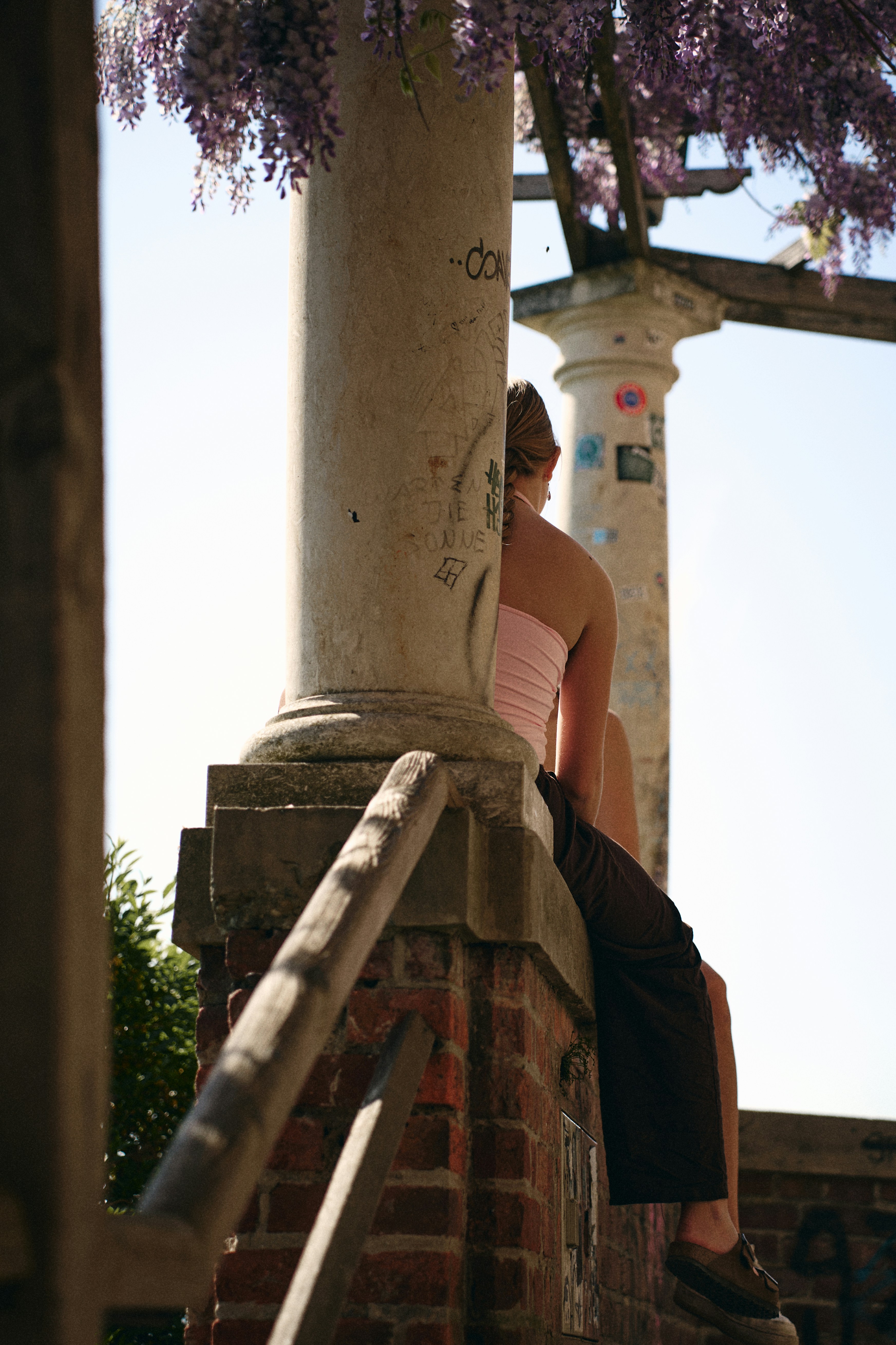 Mujer sentada en un muro de piedra bajo glicina. foto – Imagen de ...
