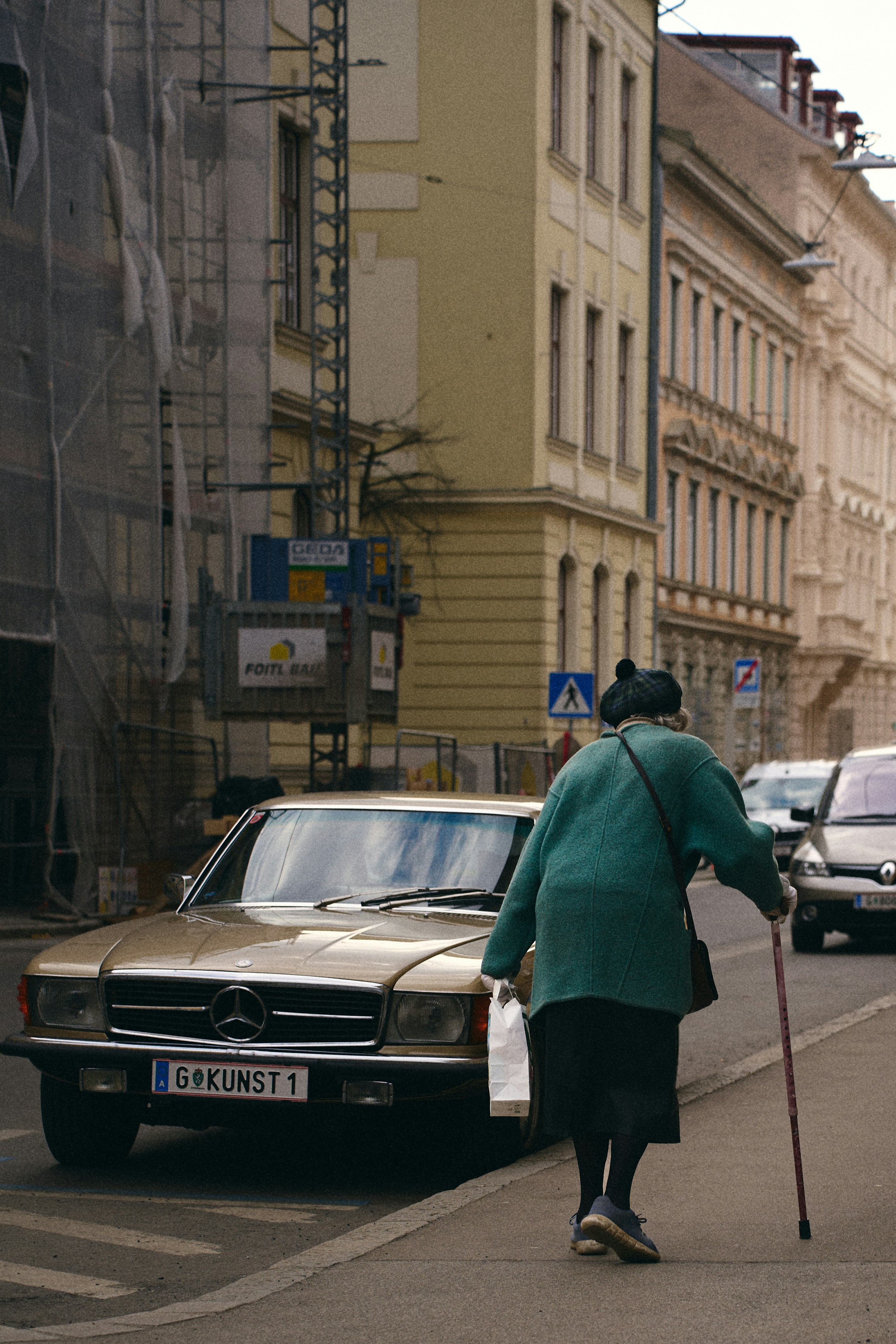 A Solitary Walk: Elderly Figure in Green Against Cityfront