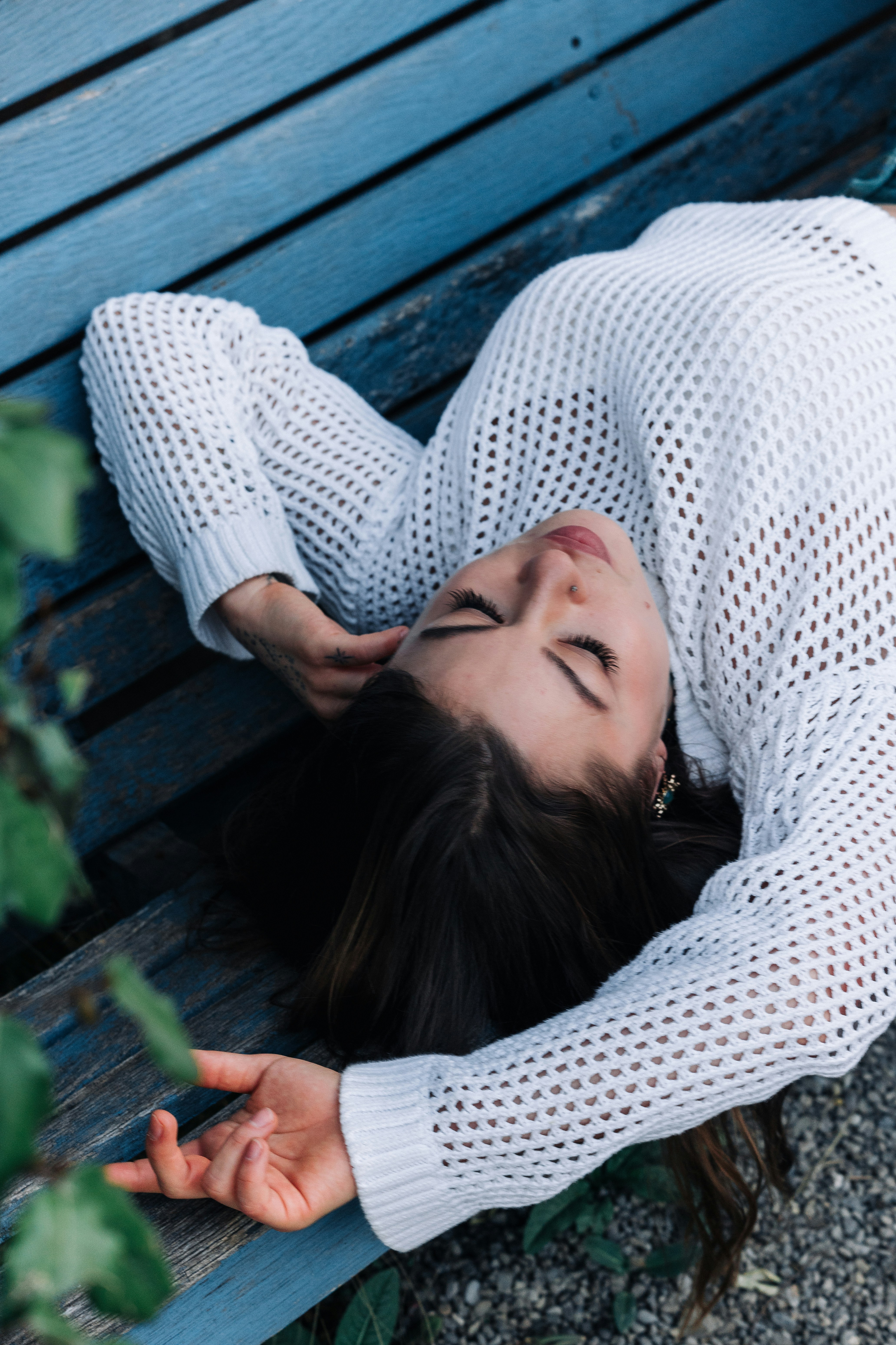 Young woman reclining on a blue wooden bench in a white mesh sweater