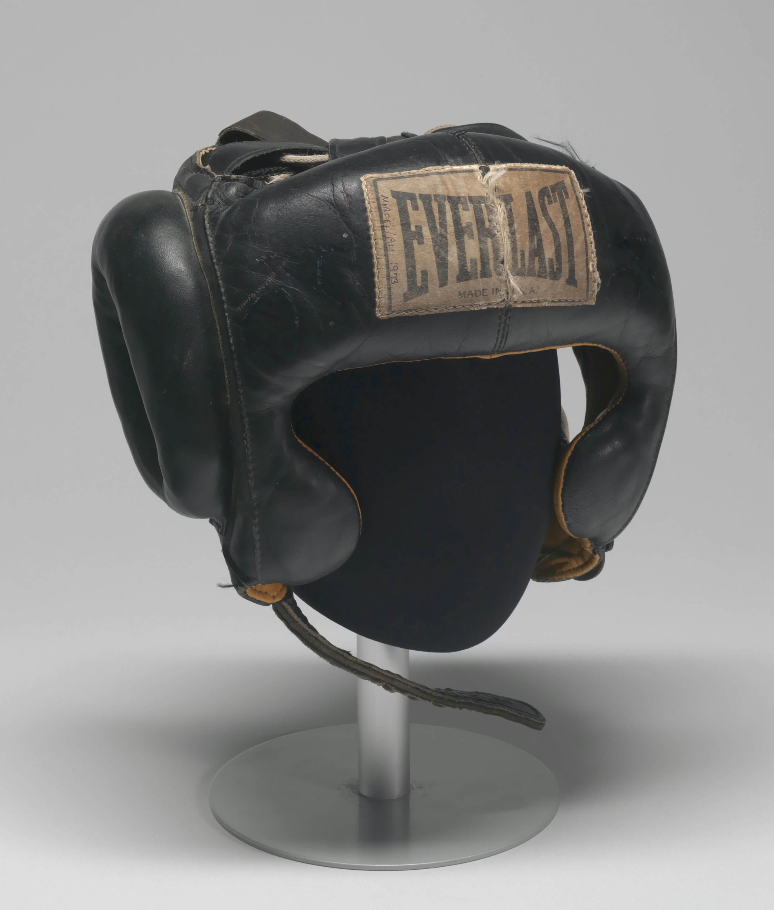 Leather boxing headgear with Everlast label sits on a stand against a neutral backdrop, emphasizing texture and vintage design.