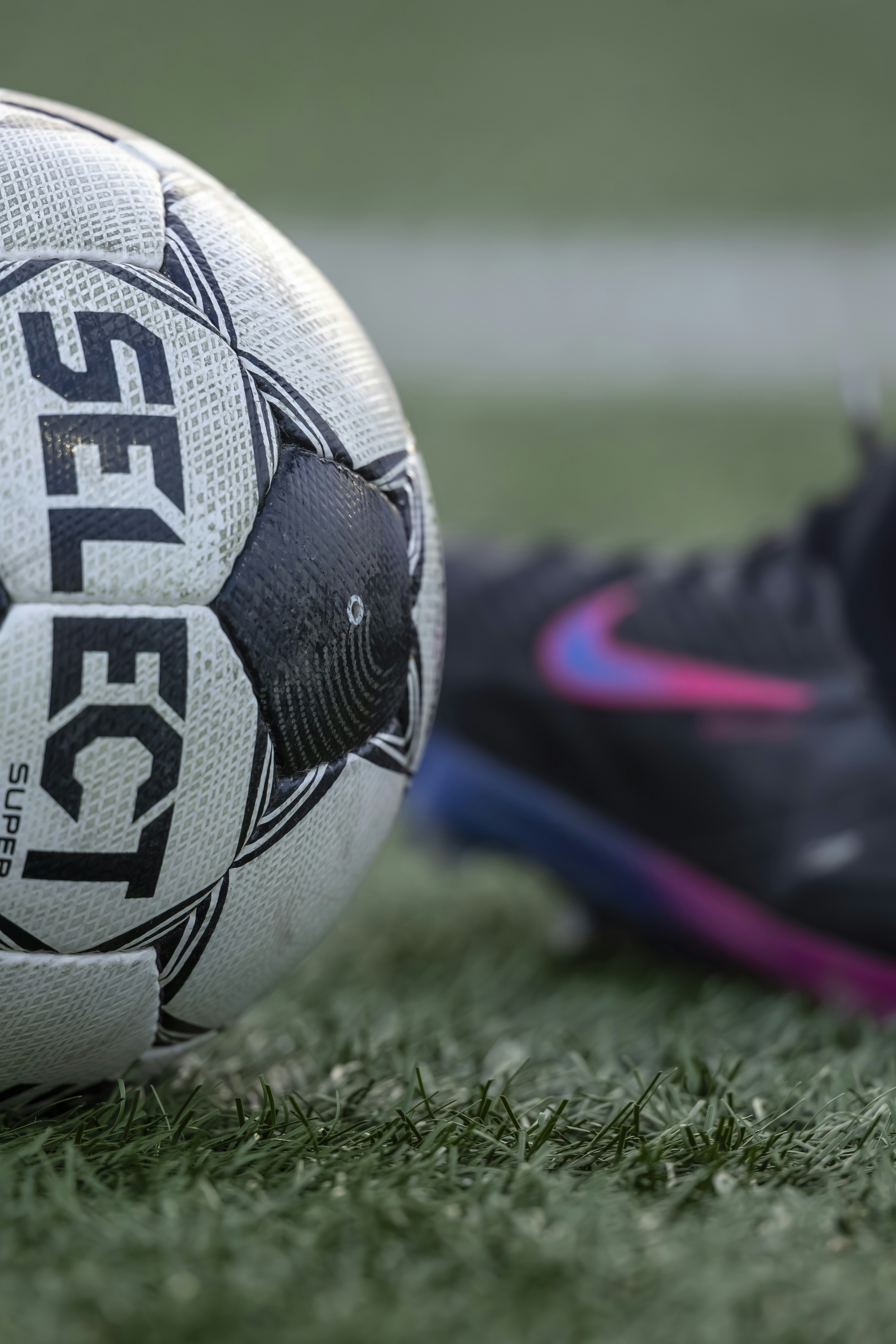Close-up of a футбольный soccer ball resting at the edge of a grass pitch with a blurred cleat in the background