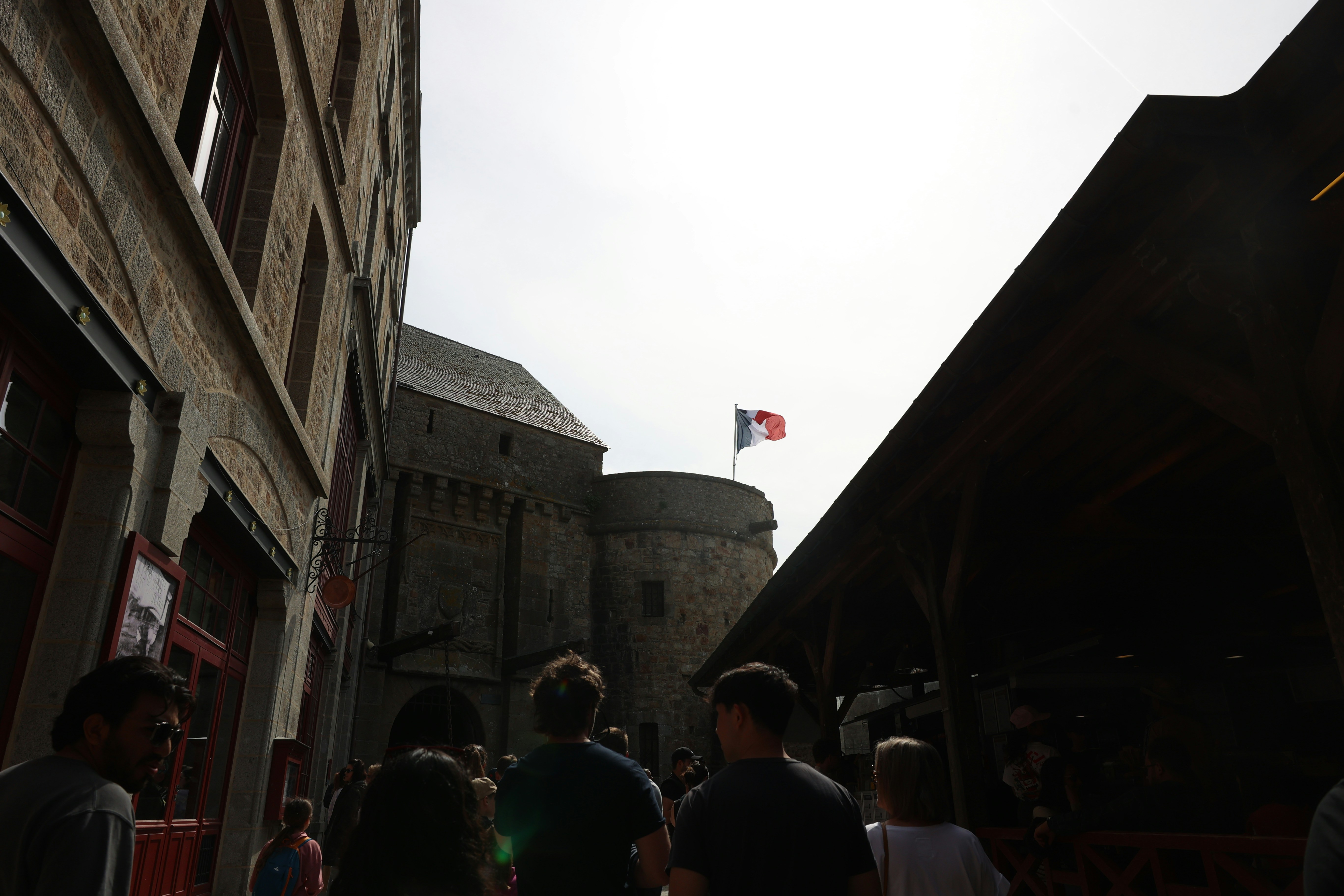 Flag Over the Medieval Gate: Morning Passengers in a Sunlit Alley
