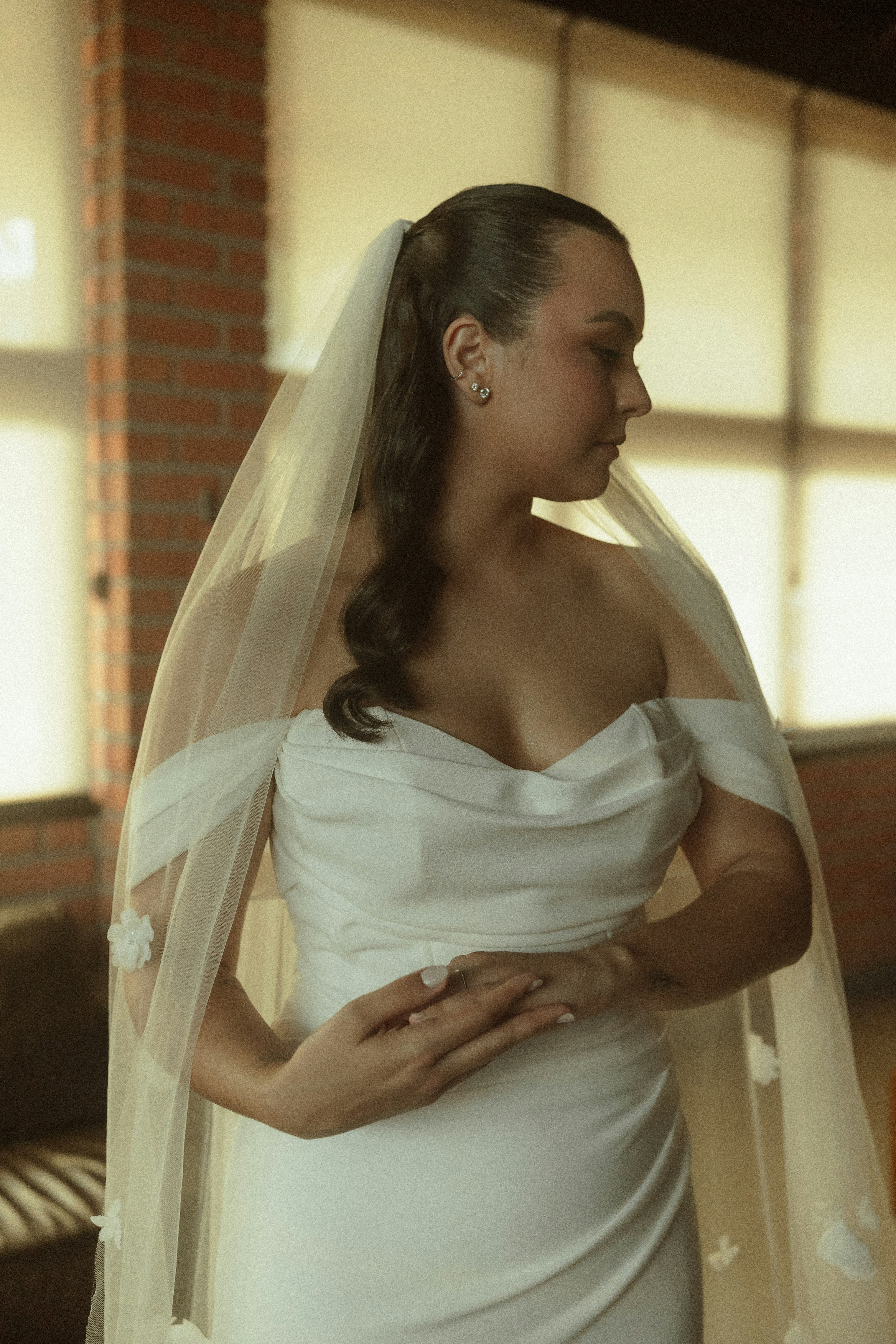 Bride in soft light: graceful pose inside brick-walled venue