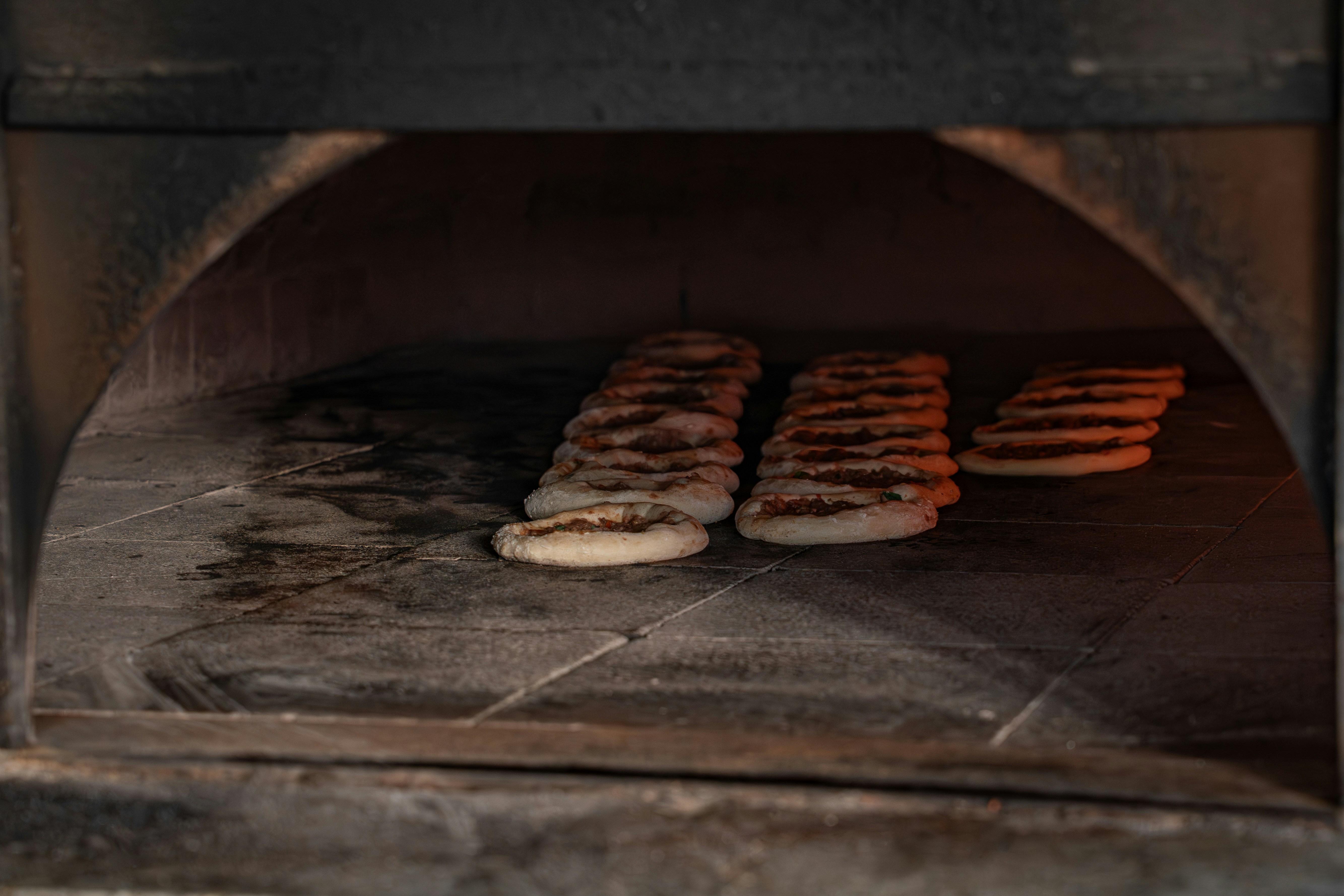 Pizzas Baking in a Wood-Fired Oven: Even Rows and Ember Glow