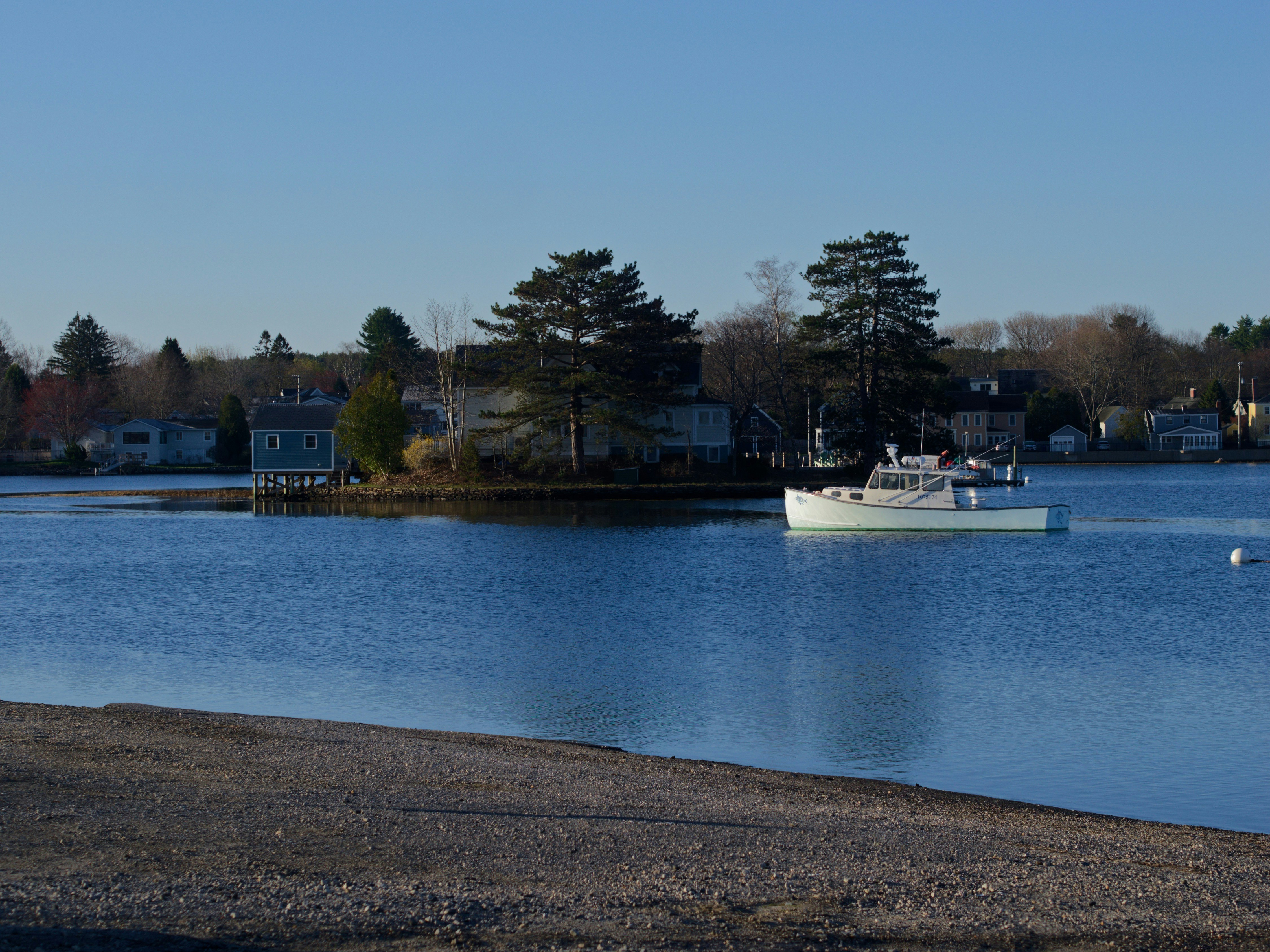 Calm harbor with a lone white boat anchored near a riverside village