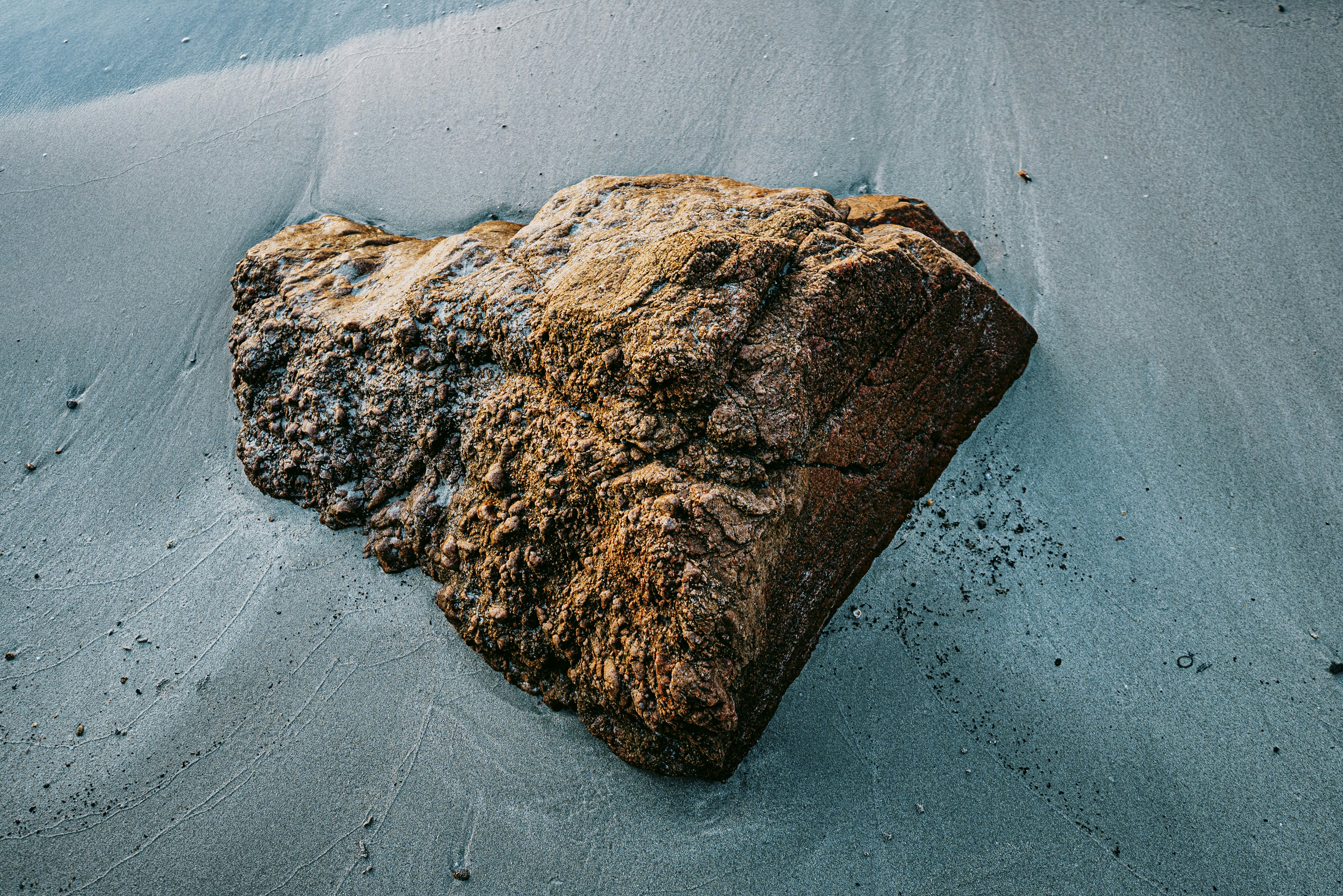 A textured rock sits on a smooth blue-toned surface, revealing earthy tones and mineral details. This image emphasizes surface texture and form without additional elements.