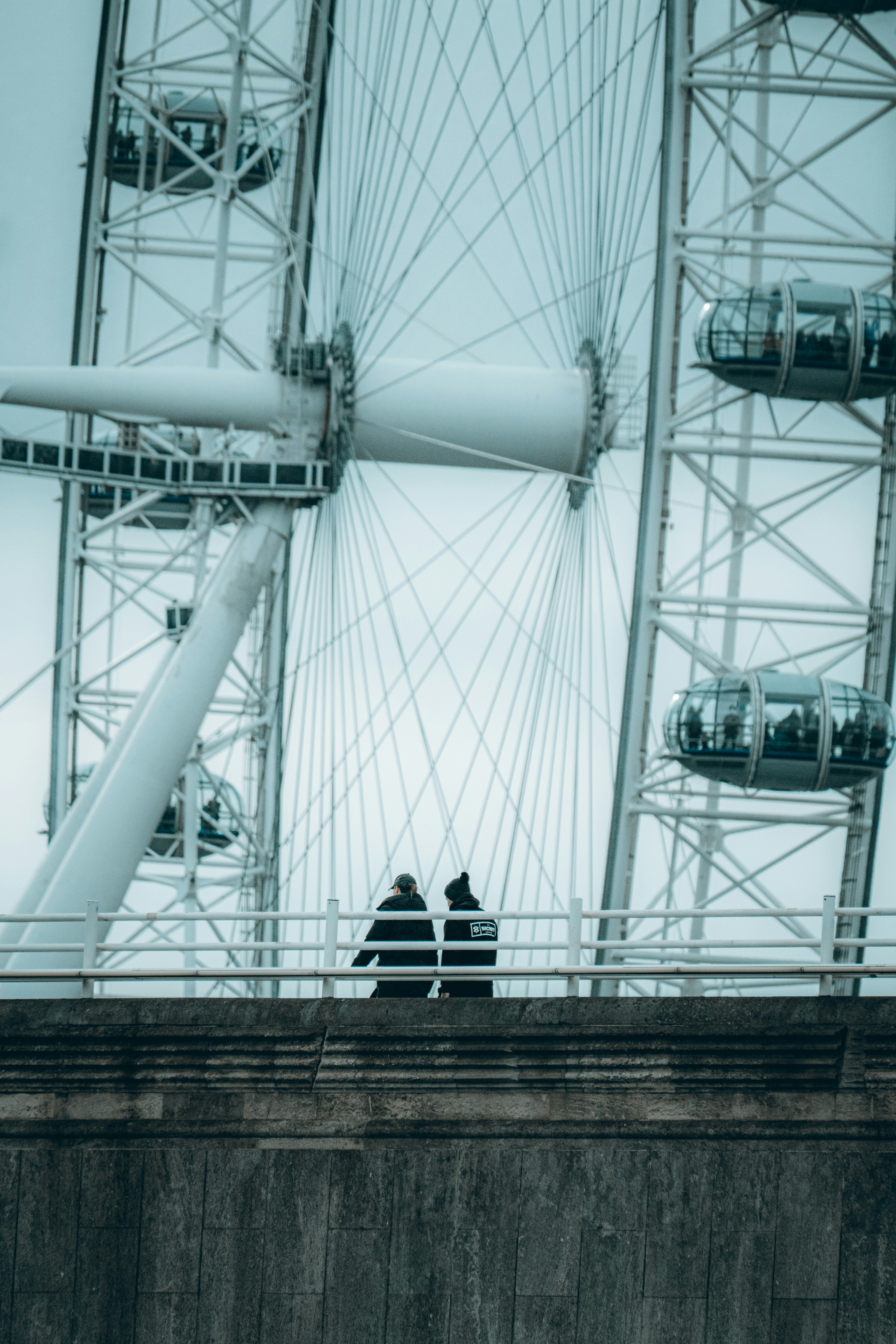 Two Silhouettes on a Spoked Skywalk Beneath a Giant London Eye Structure