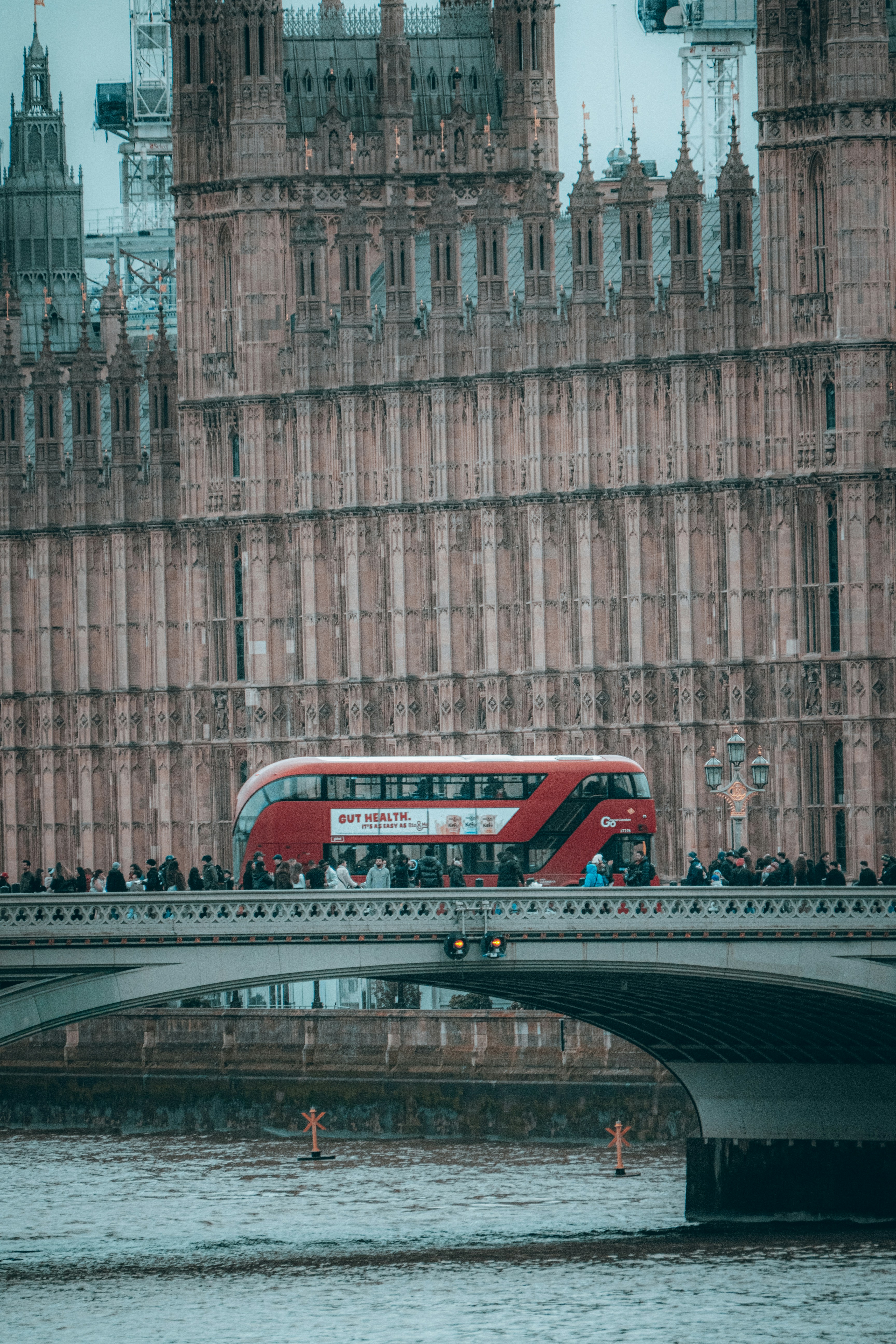 Scarlet Bus on the Thames Bridge Beneath Gothic Facades
