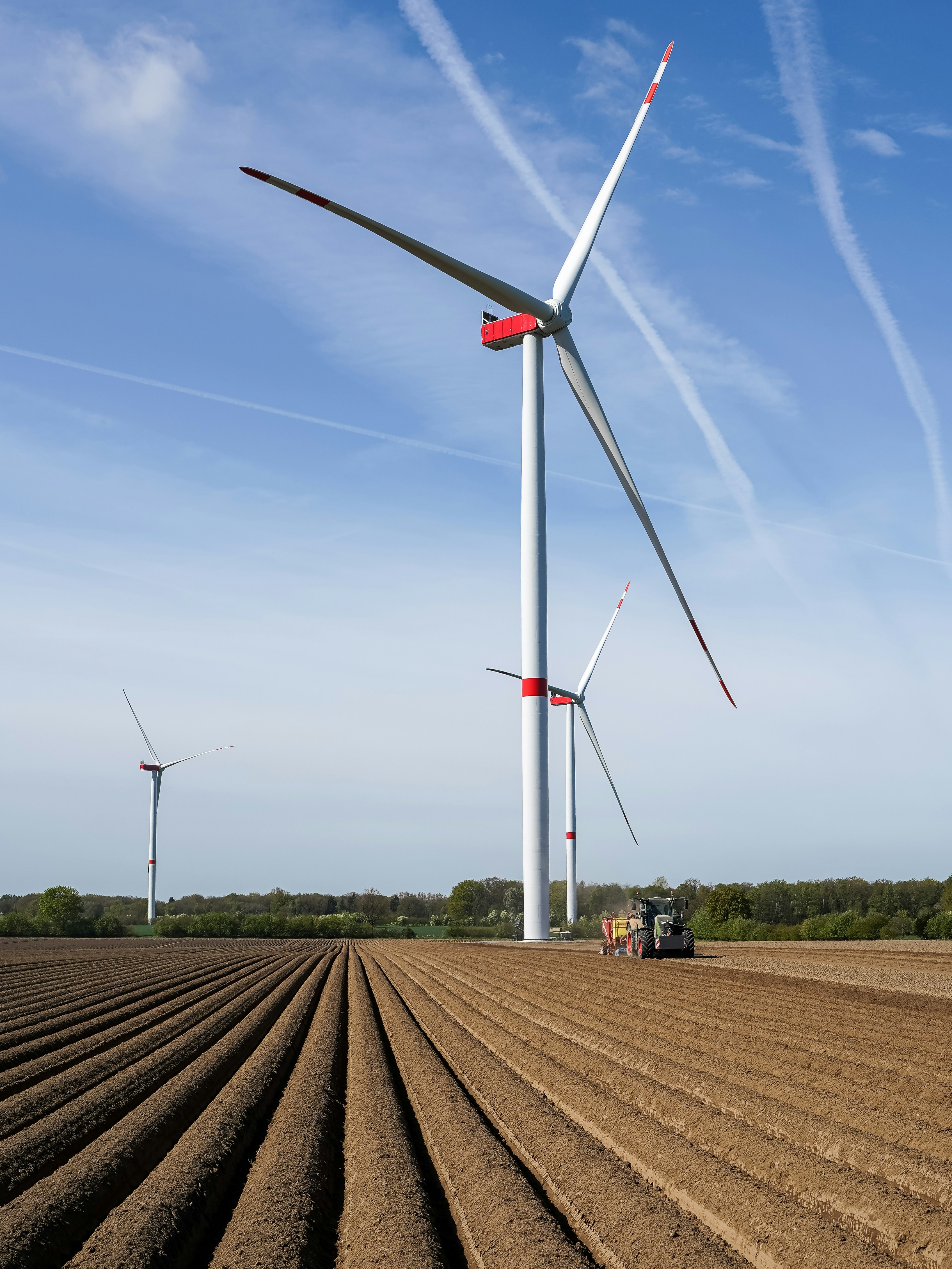 Giant Wind Turbine Emerges Over Plowed Fields at Distant Horizon