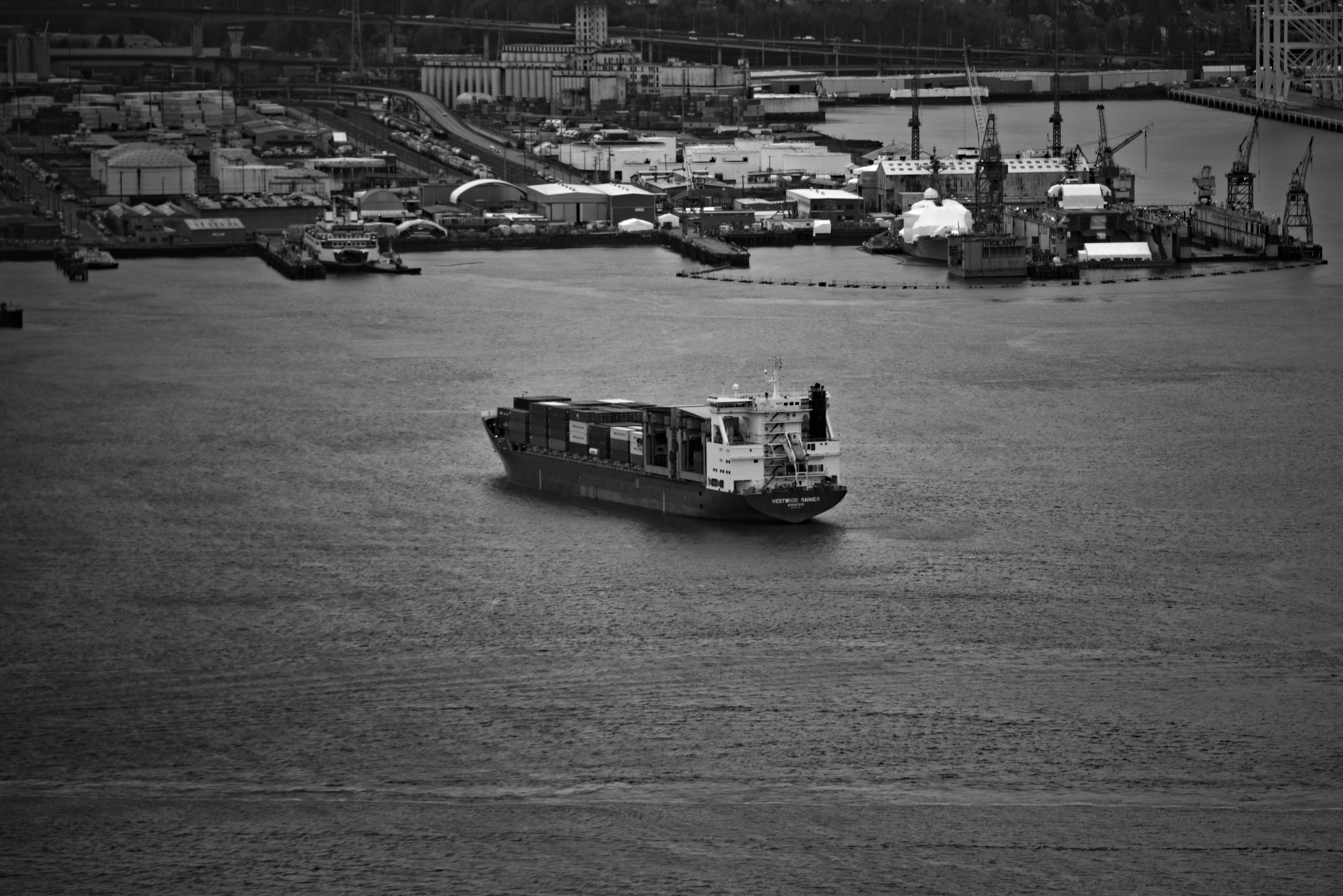 Harbor Barque: A lone cargo vessel glides through a grayscale city harbor