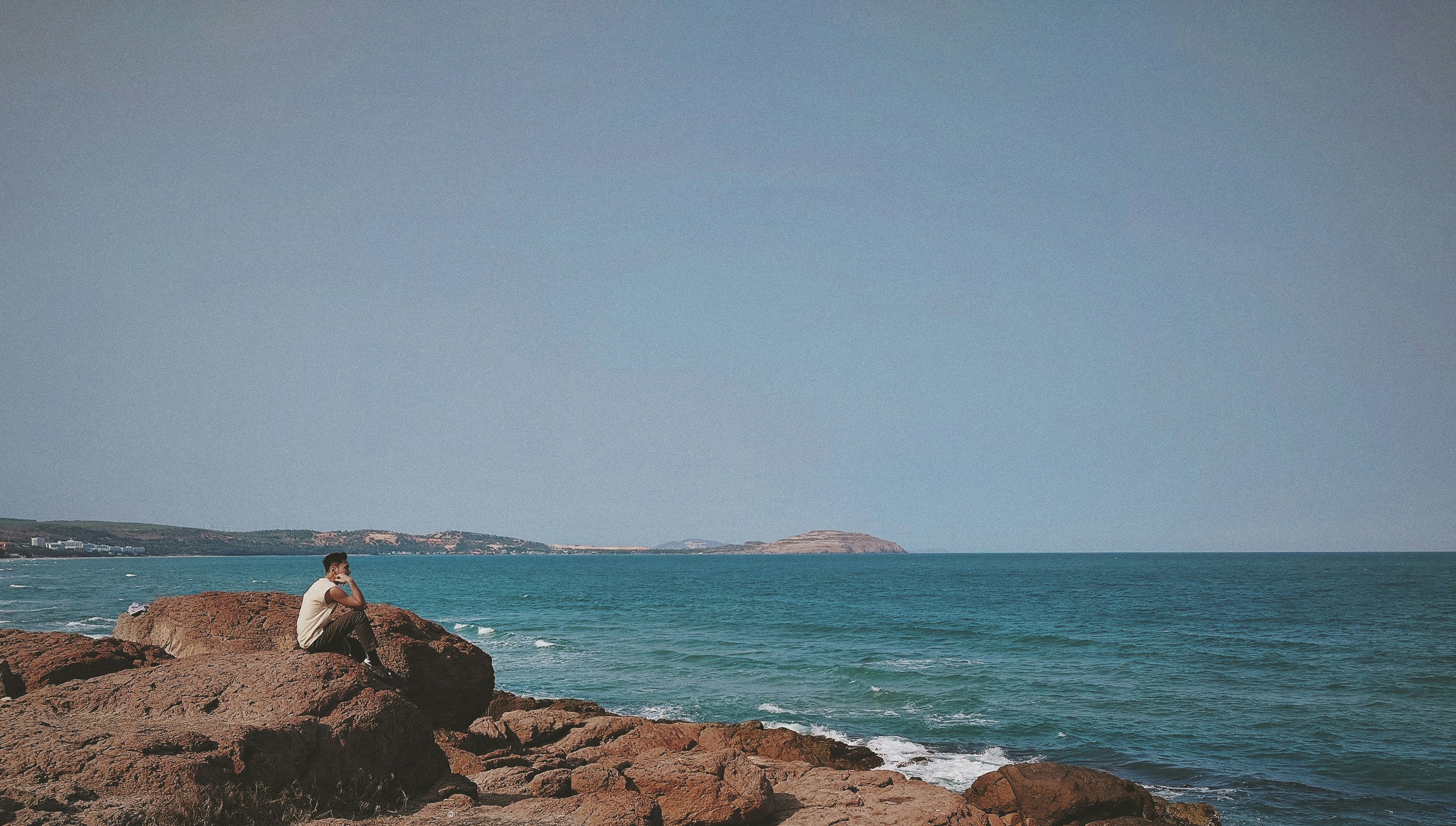 Solitary Figure on Weathered Red Rocks Beneath a Calm Horizon