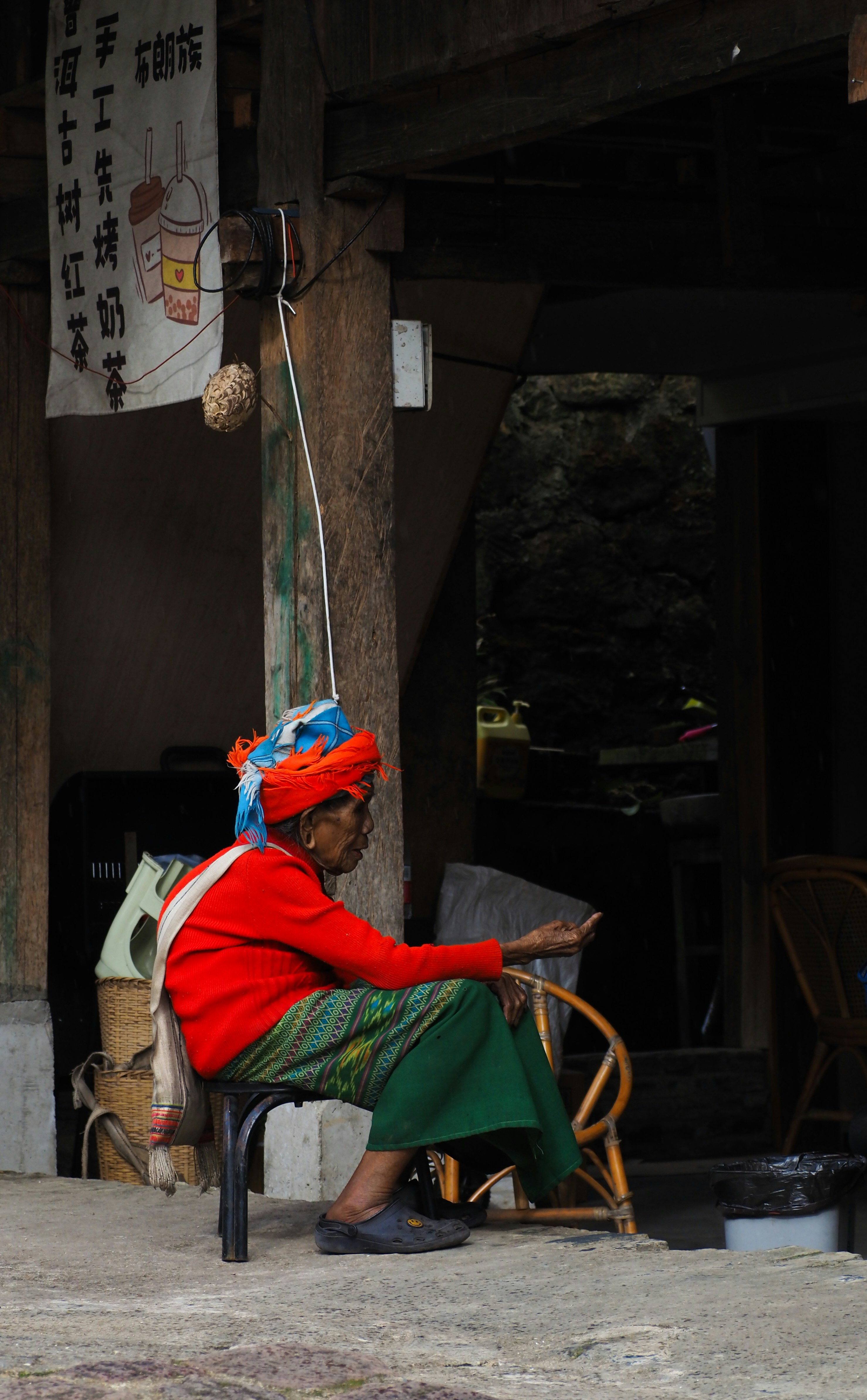 Older woman in red sweater rests on a bench inside a rustic doorway