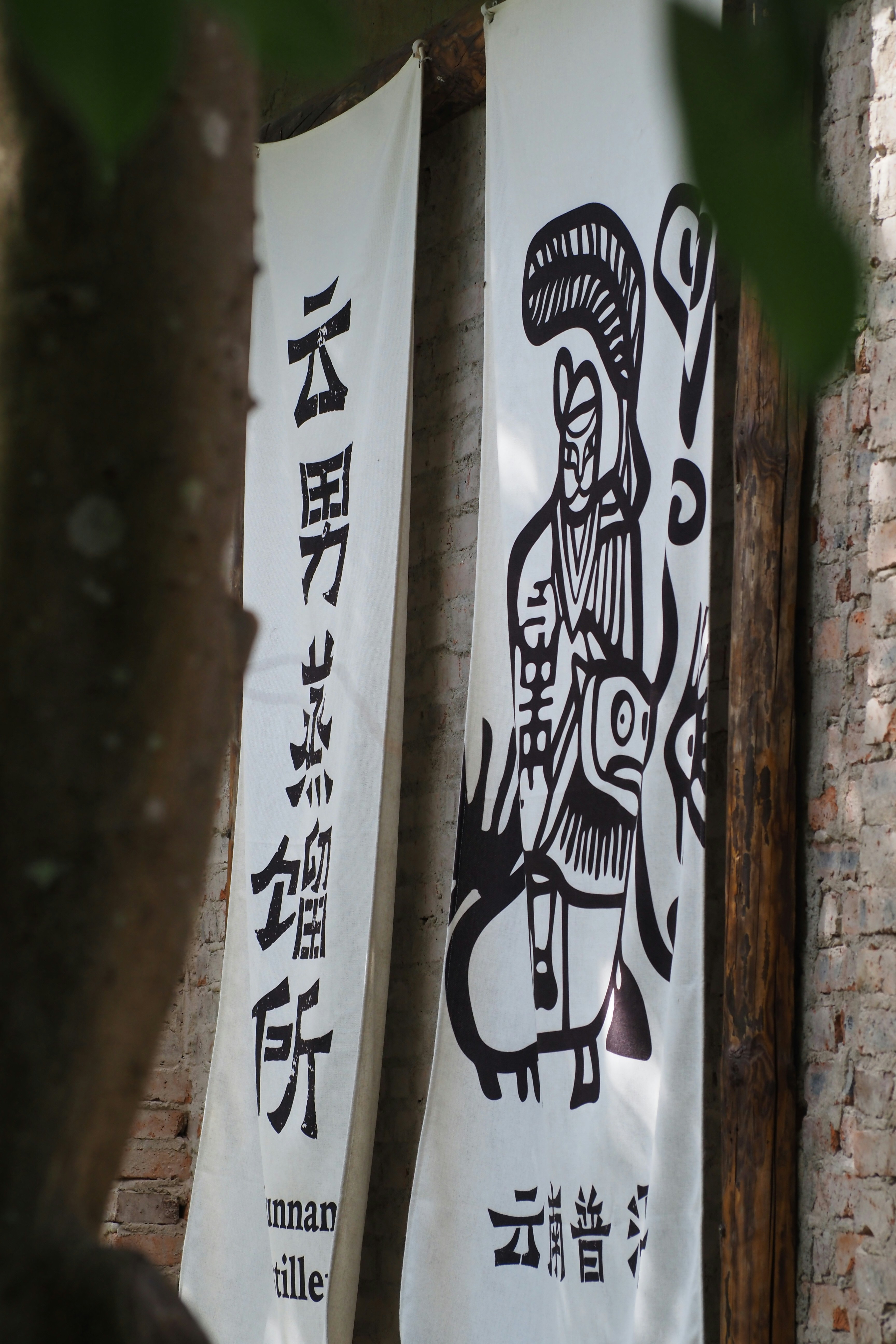 Vertical banners inked with bold figures lean against a sunlit brick wall