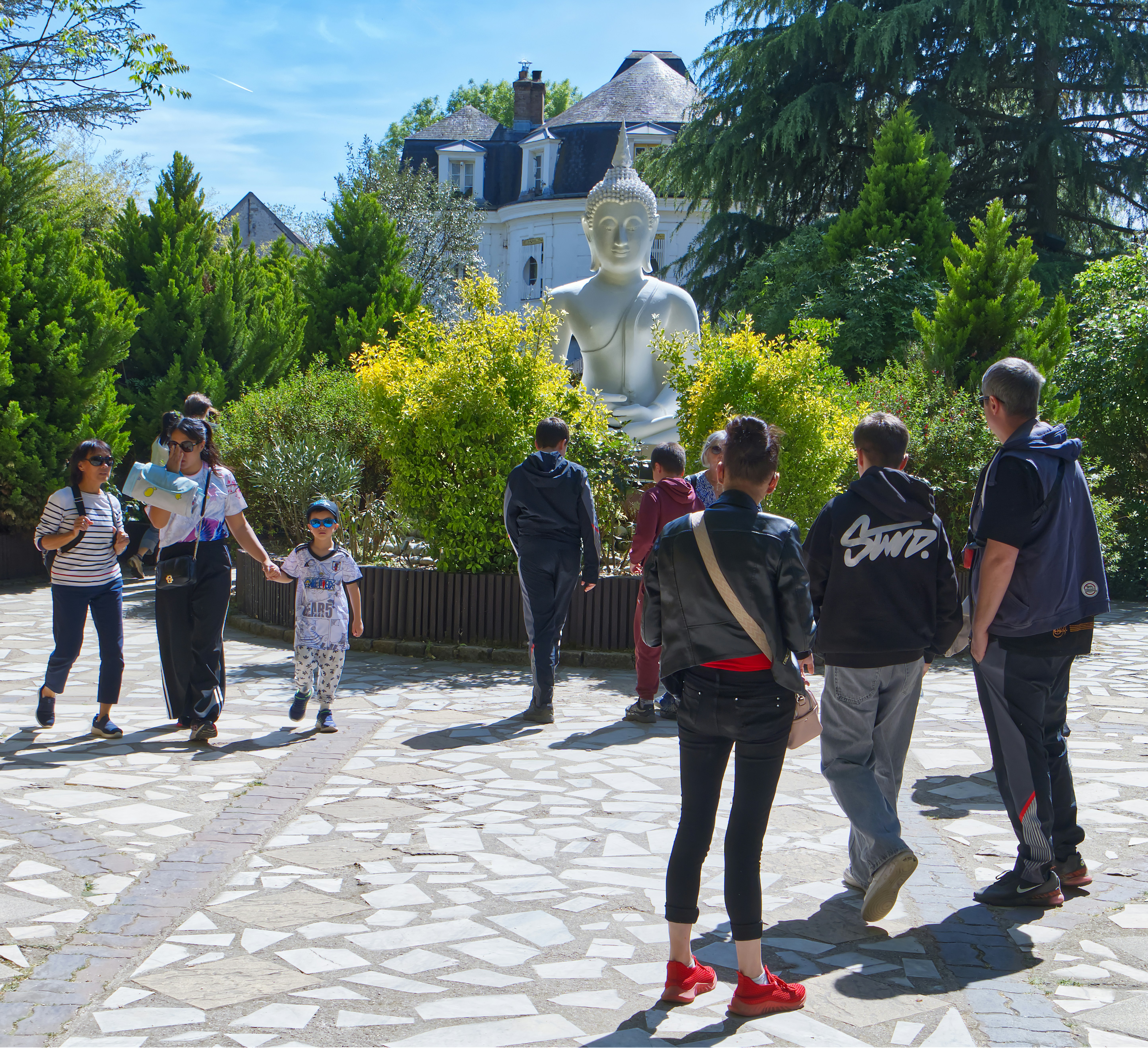 Visitors Gather Around a Serene Garden with a Buddha Statue Backdrop