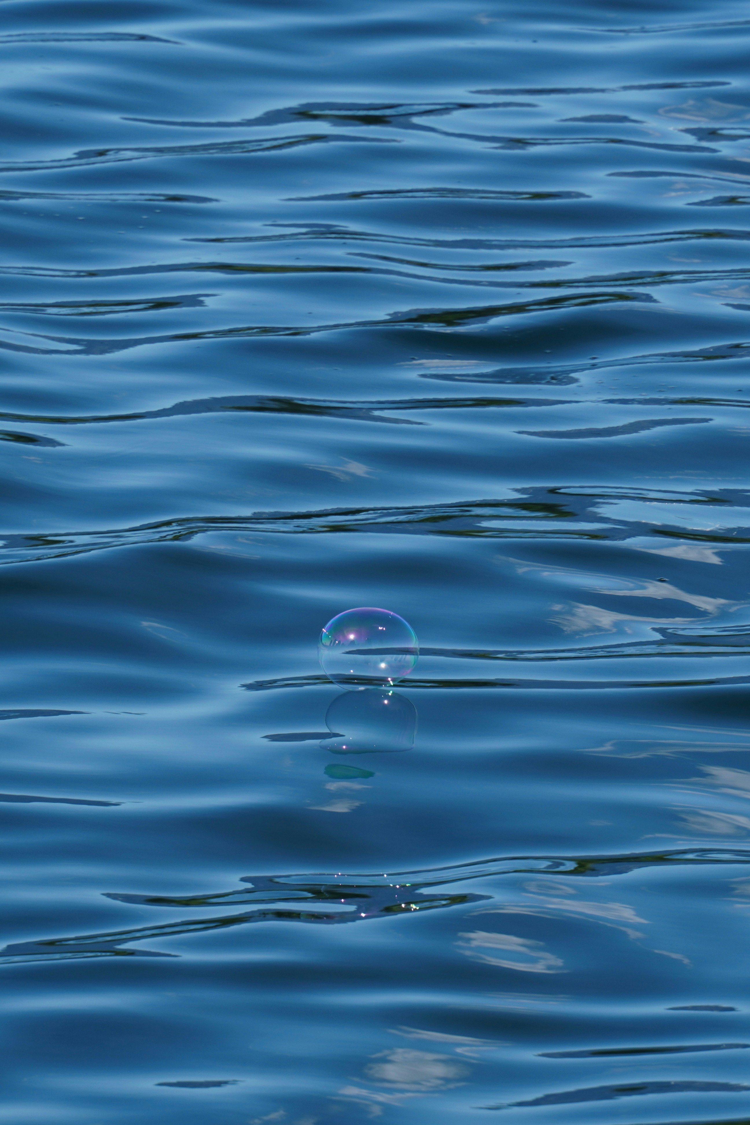 Reflections on a Glassy Lake: a Bubble Drifts Against Blue Ripples