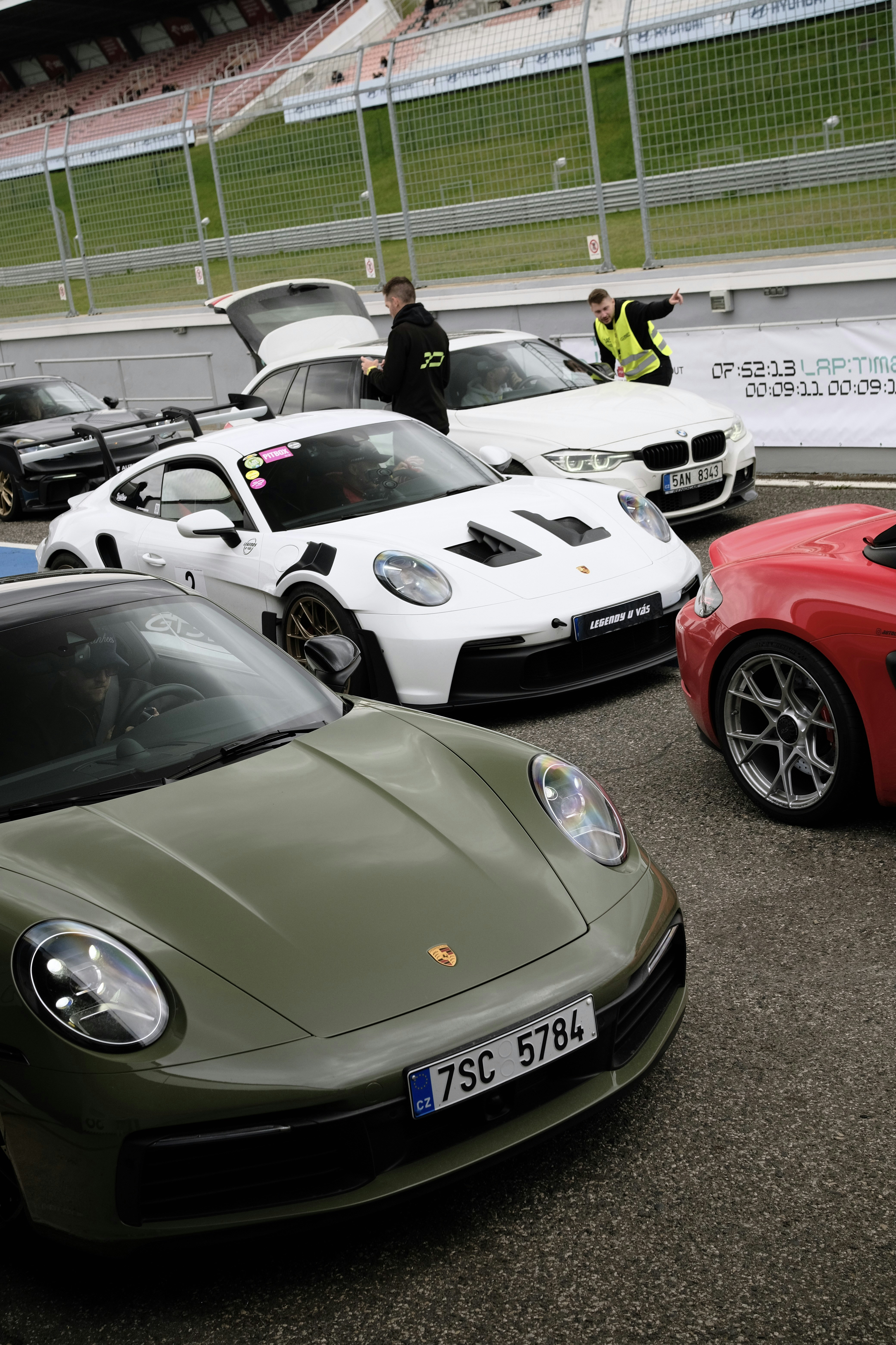 Pit Lane Portrait: White Porsche Cayman Amongst Exotics at the Track