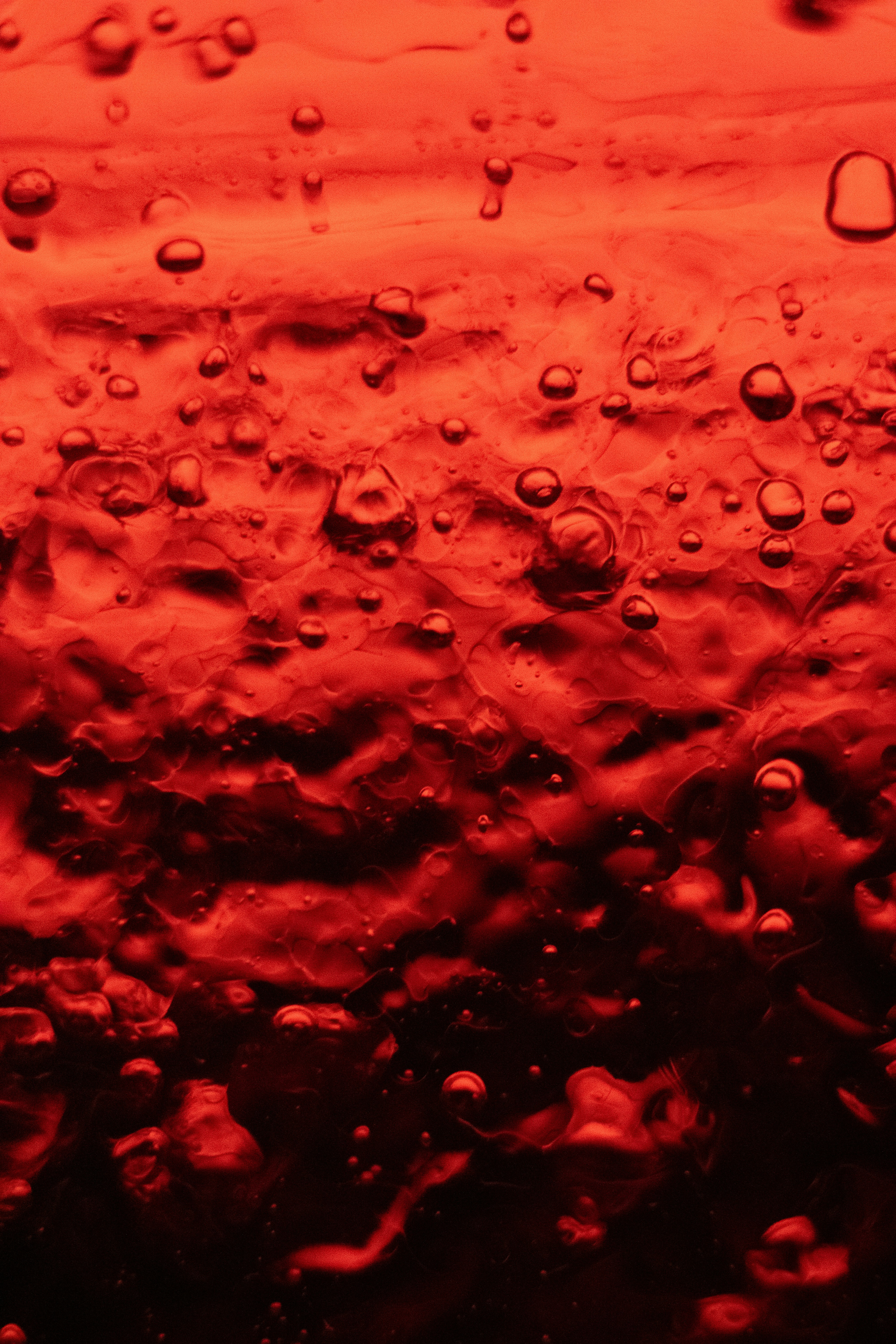 Intense red-toned macro of bubbling liquid with varying bubble sizes and swirling textures, emphasizing motion and depth.