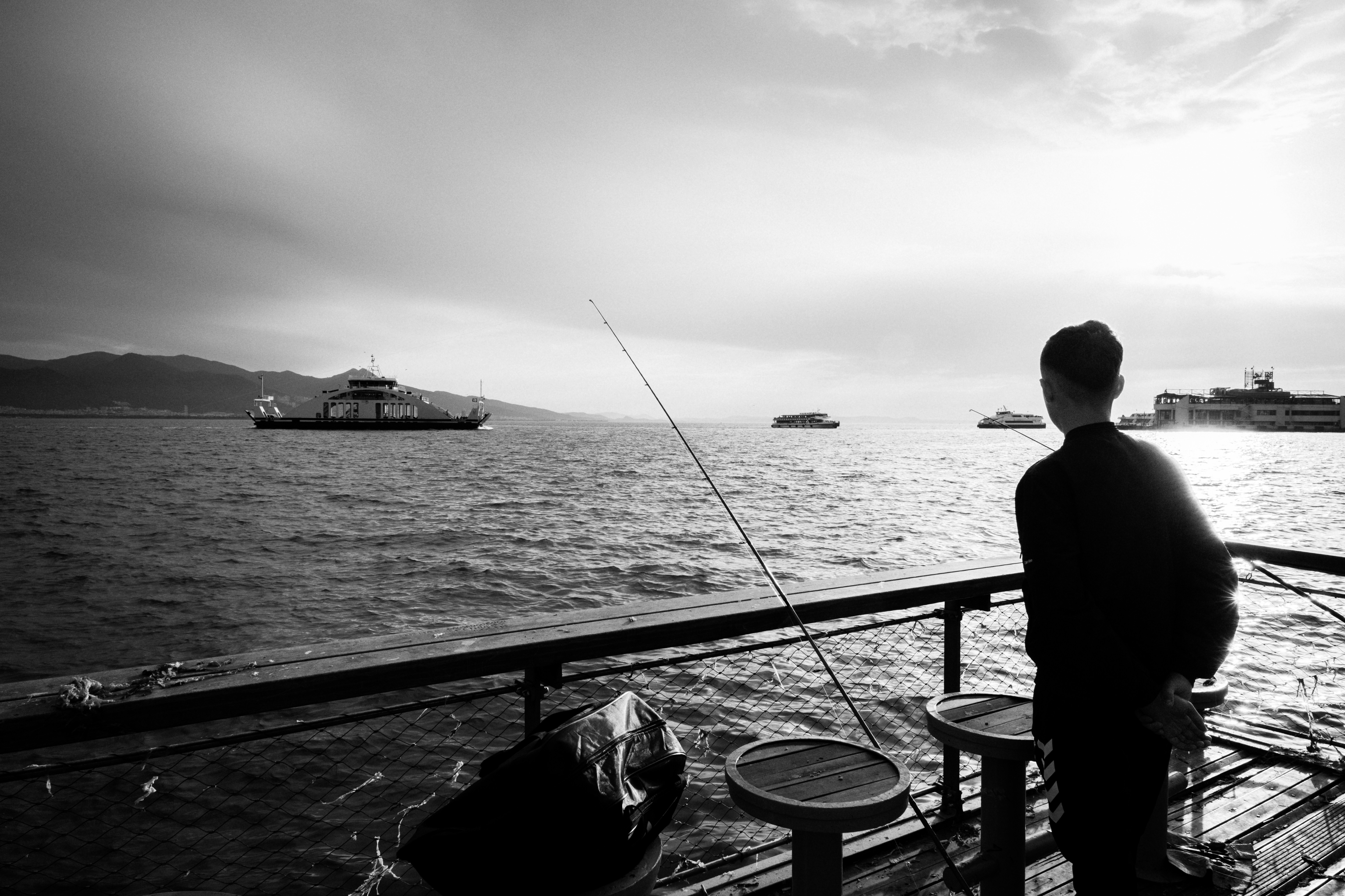 Silhouette at the Seawall: A Quiet Moment by the Distant Fleet