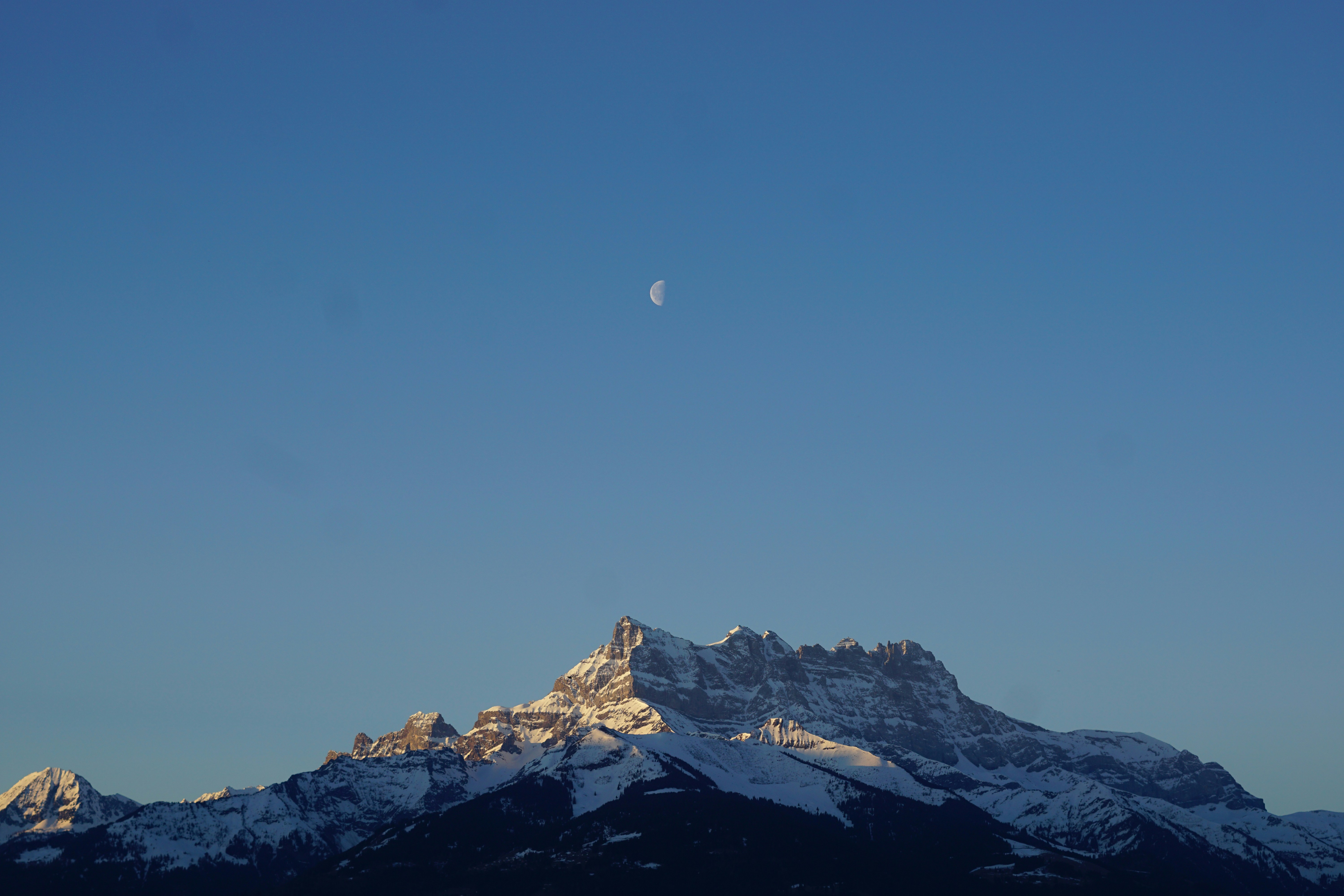 Moonlit Crest: Snow-Capped Peak Under Diminutive Moon