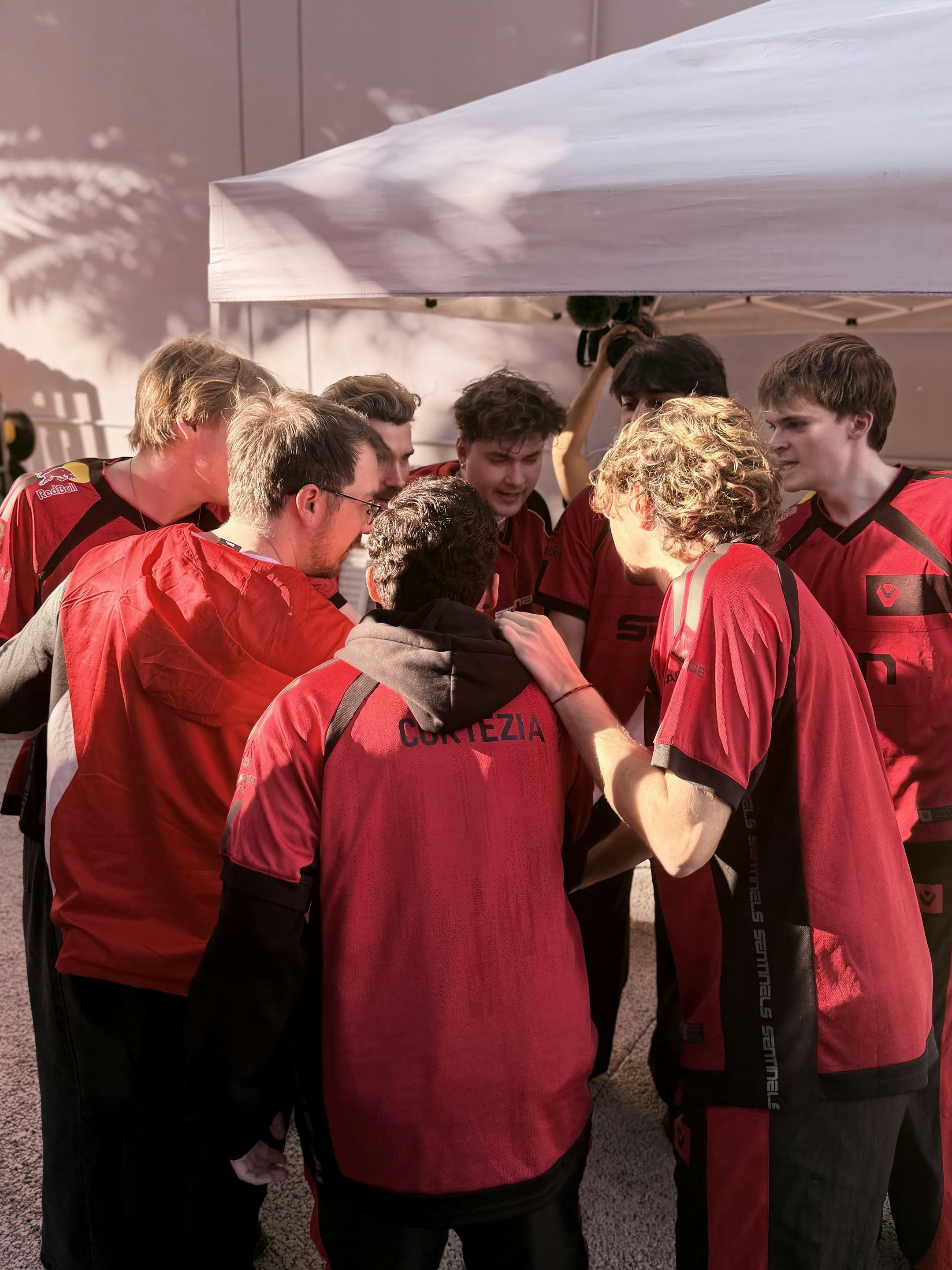 Team Huddle Under White Canopy: Red Jerseys in Close Assembly