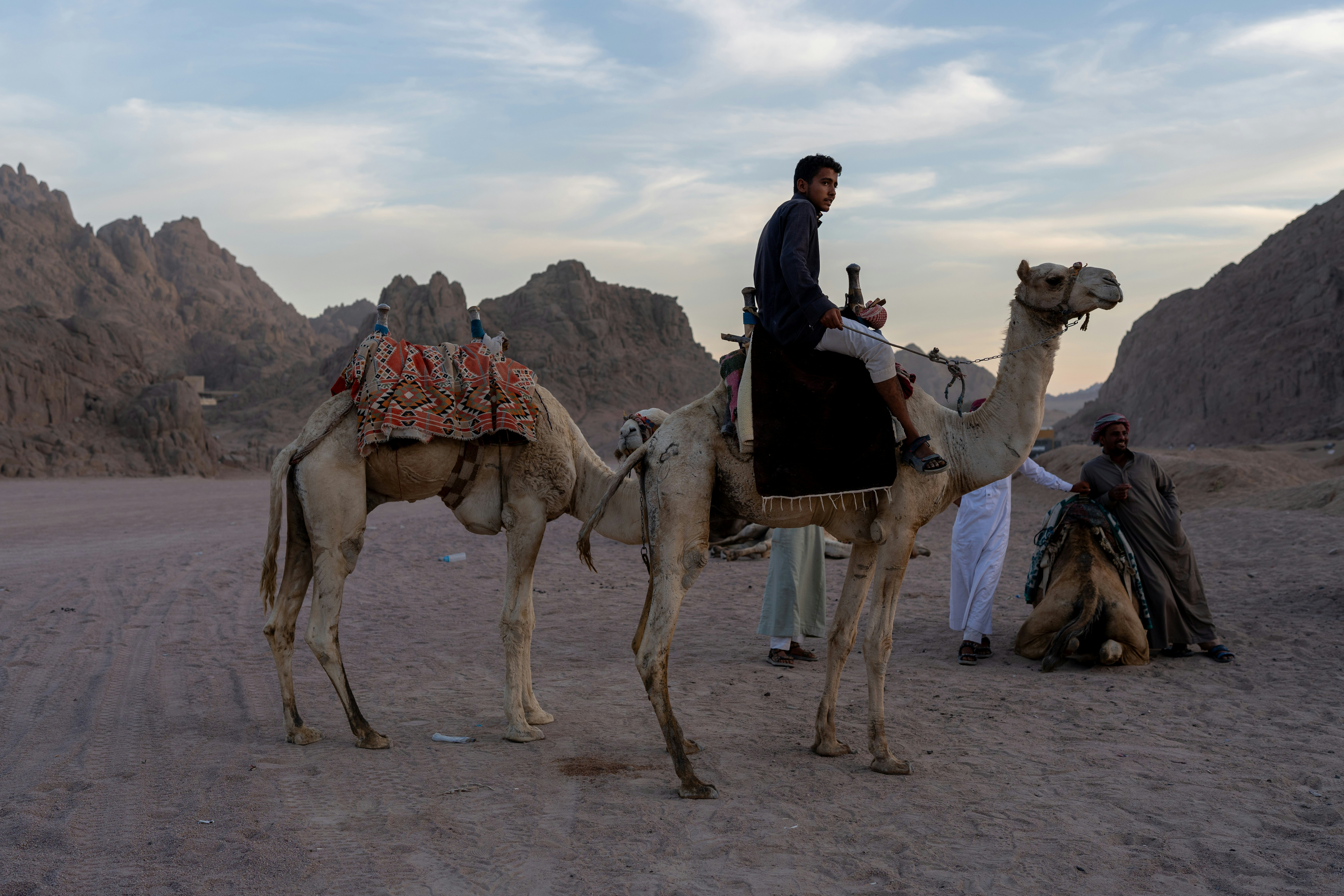 Dune Roadscape: Riders and Camels Amidst Rugged Peaks