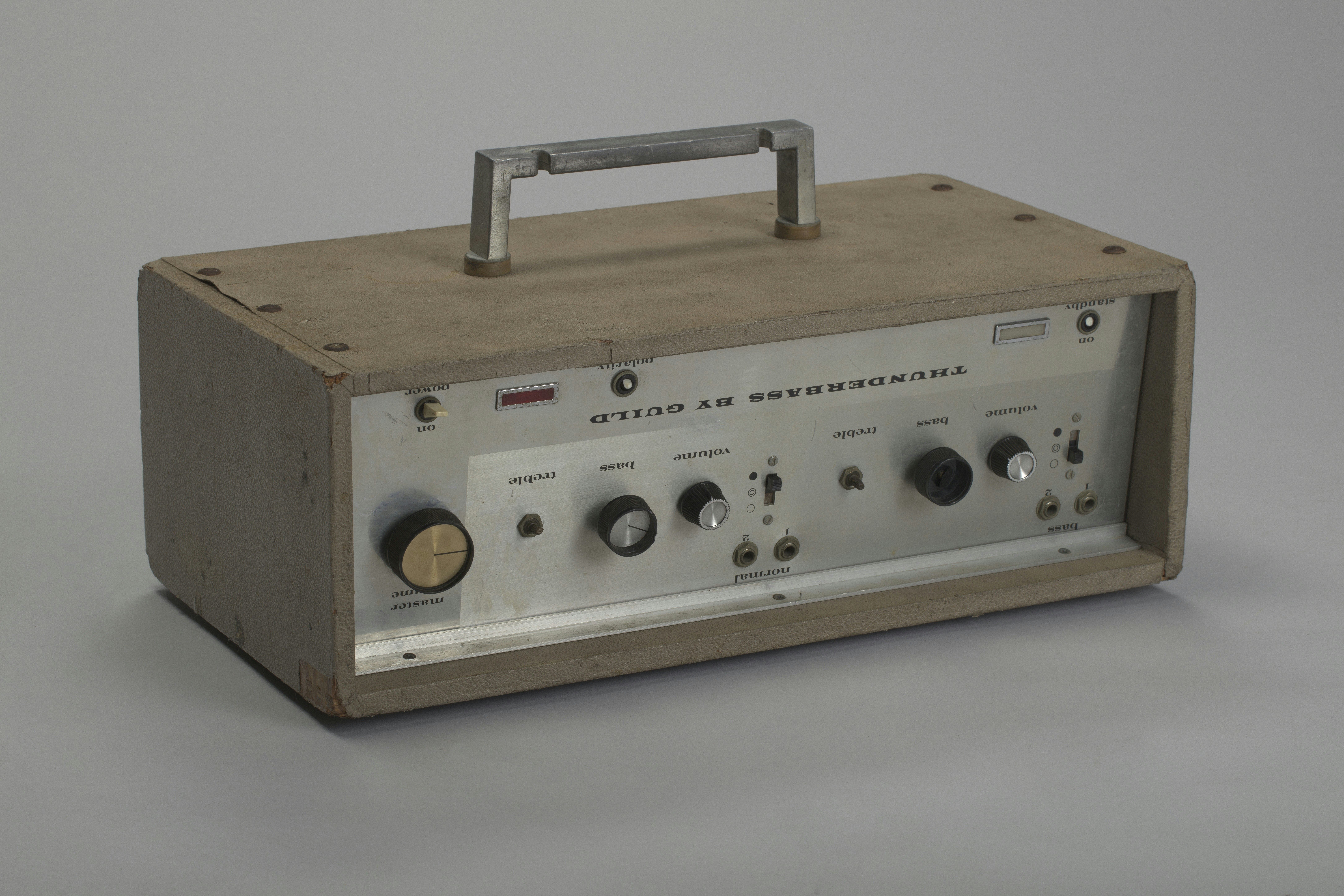 A weathered vintage lab amplifier sits on a neutral backdrop, its worn wood case and metal faceplate telling stories of decades of use.
