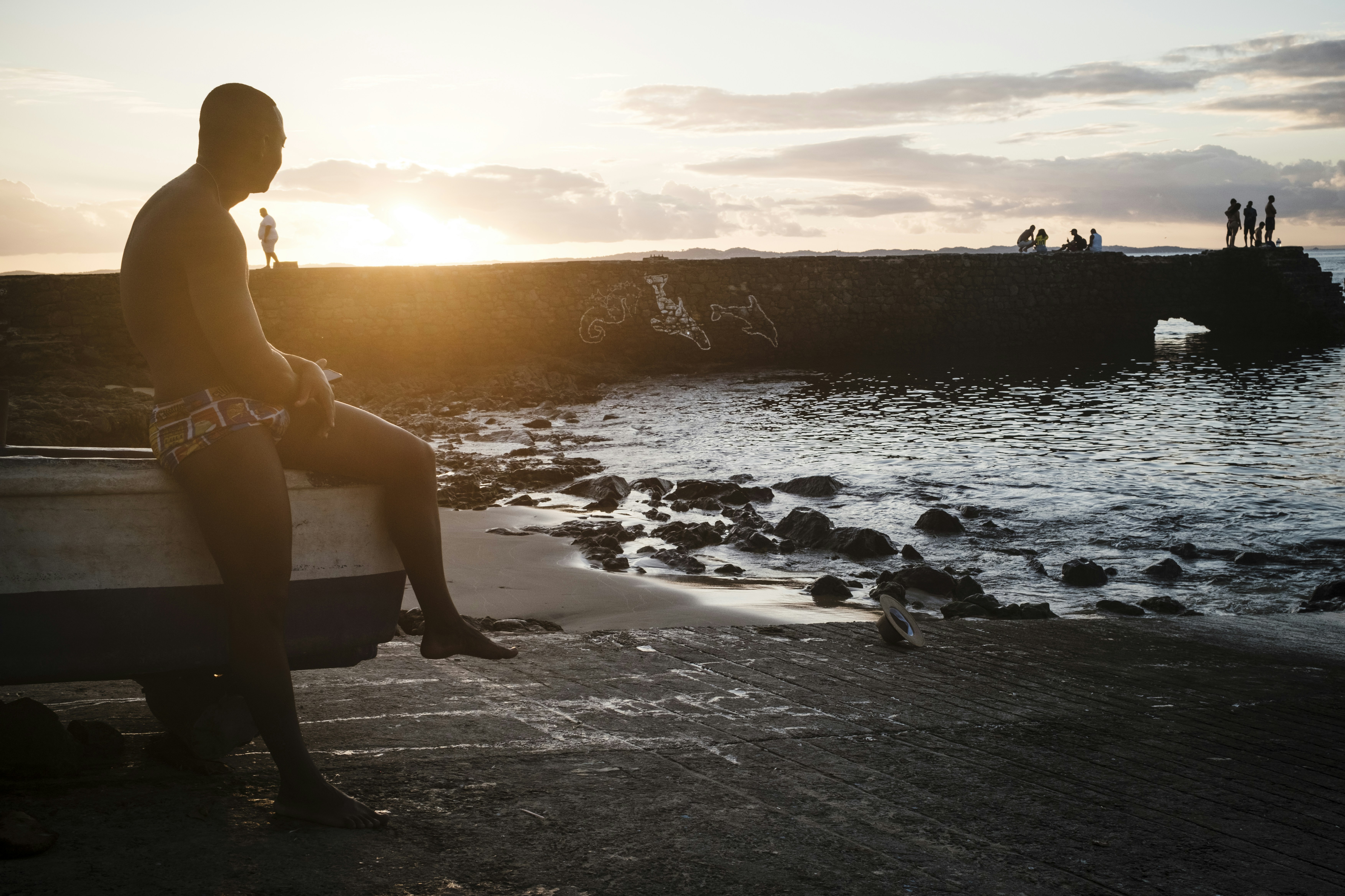 Sunlit silhouette: man seated on jetty at golden hour