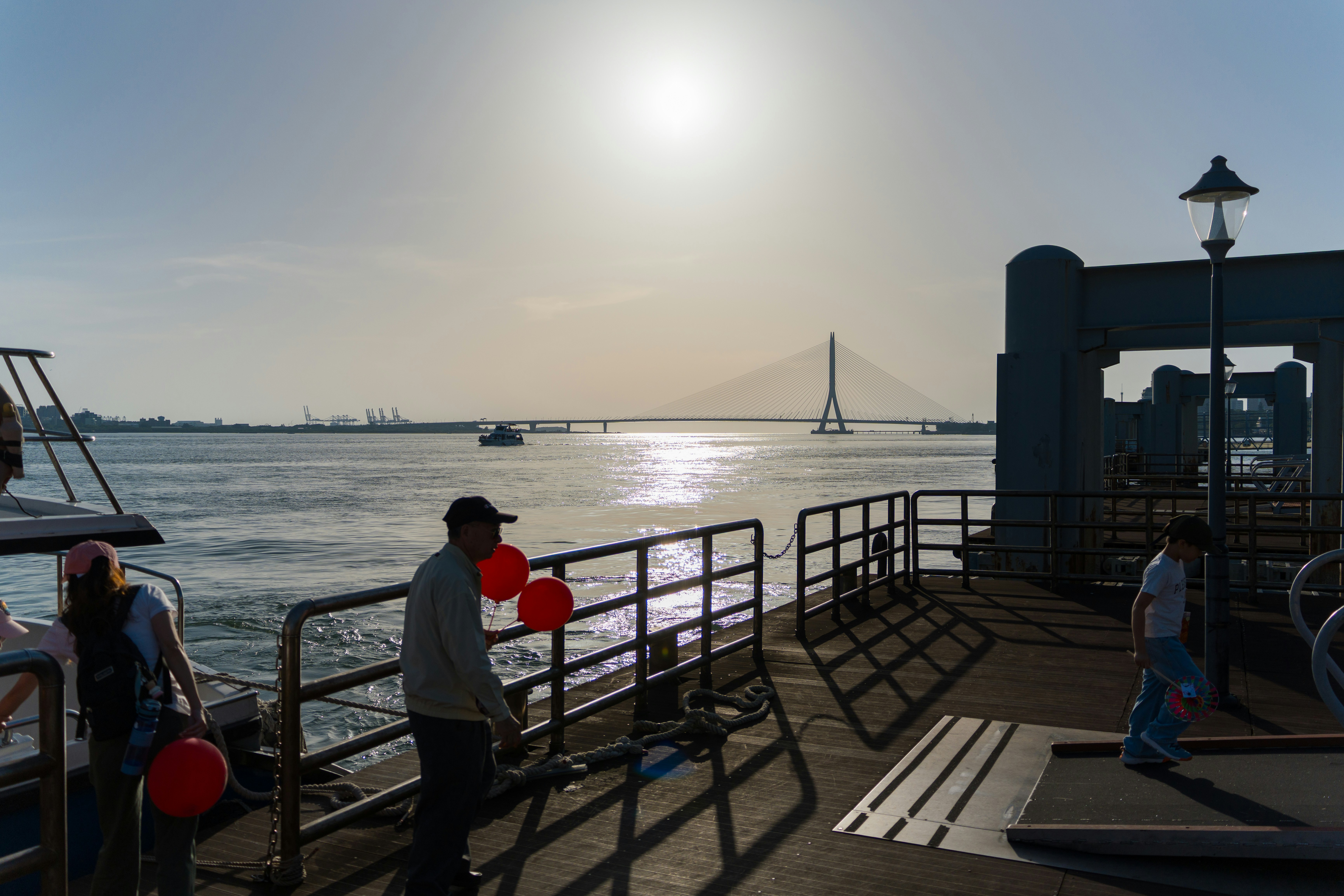 Sunlit Pier Portrait: People, Balloons, and Distant Skyline