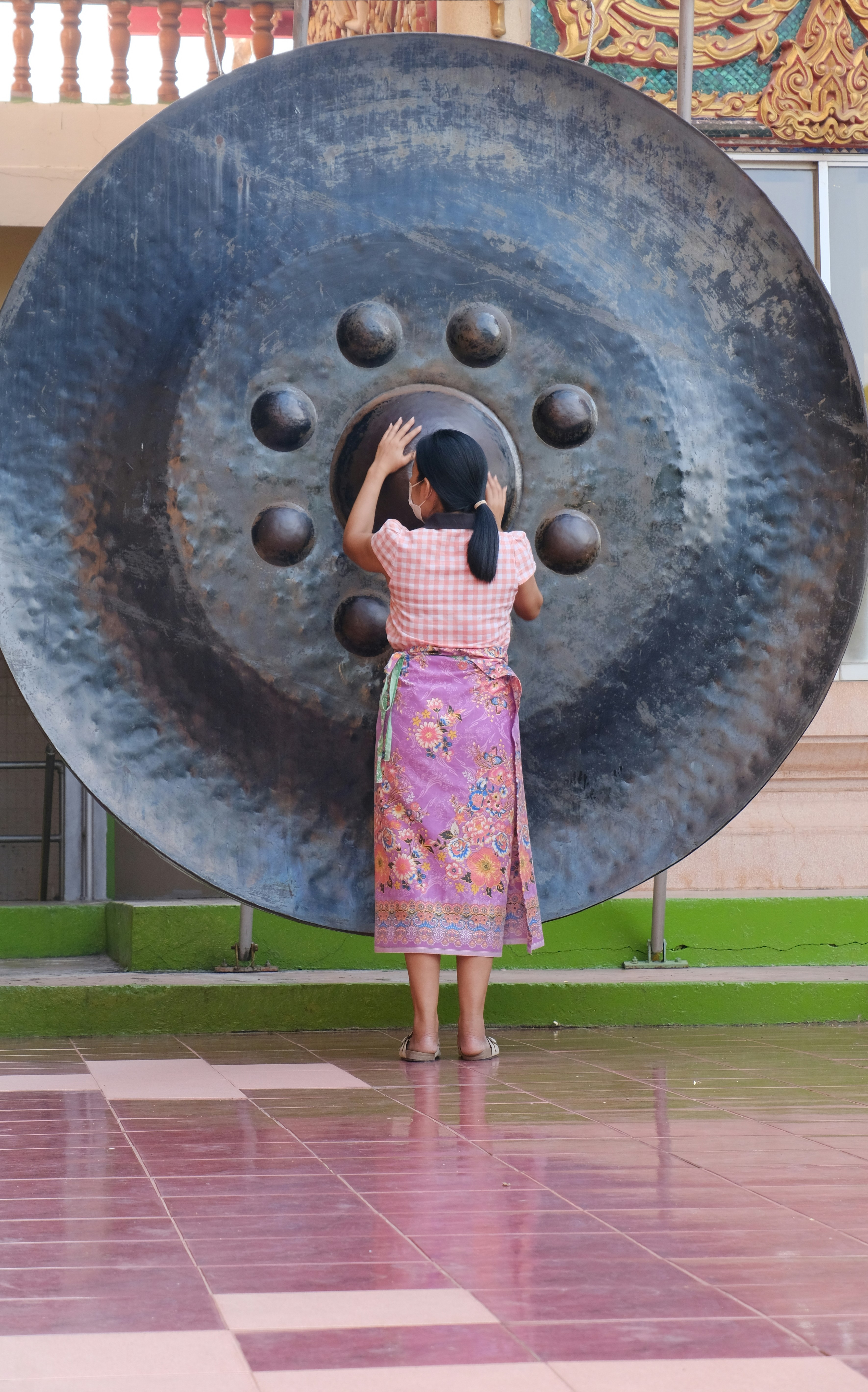 Holding Silence: A girl in a pink blouse and sash finds calm against a giant drum