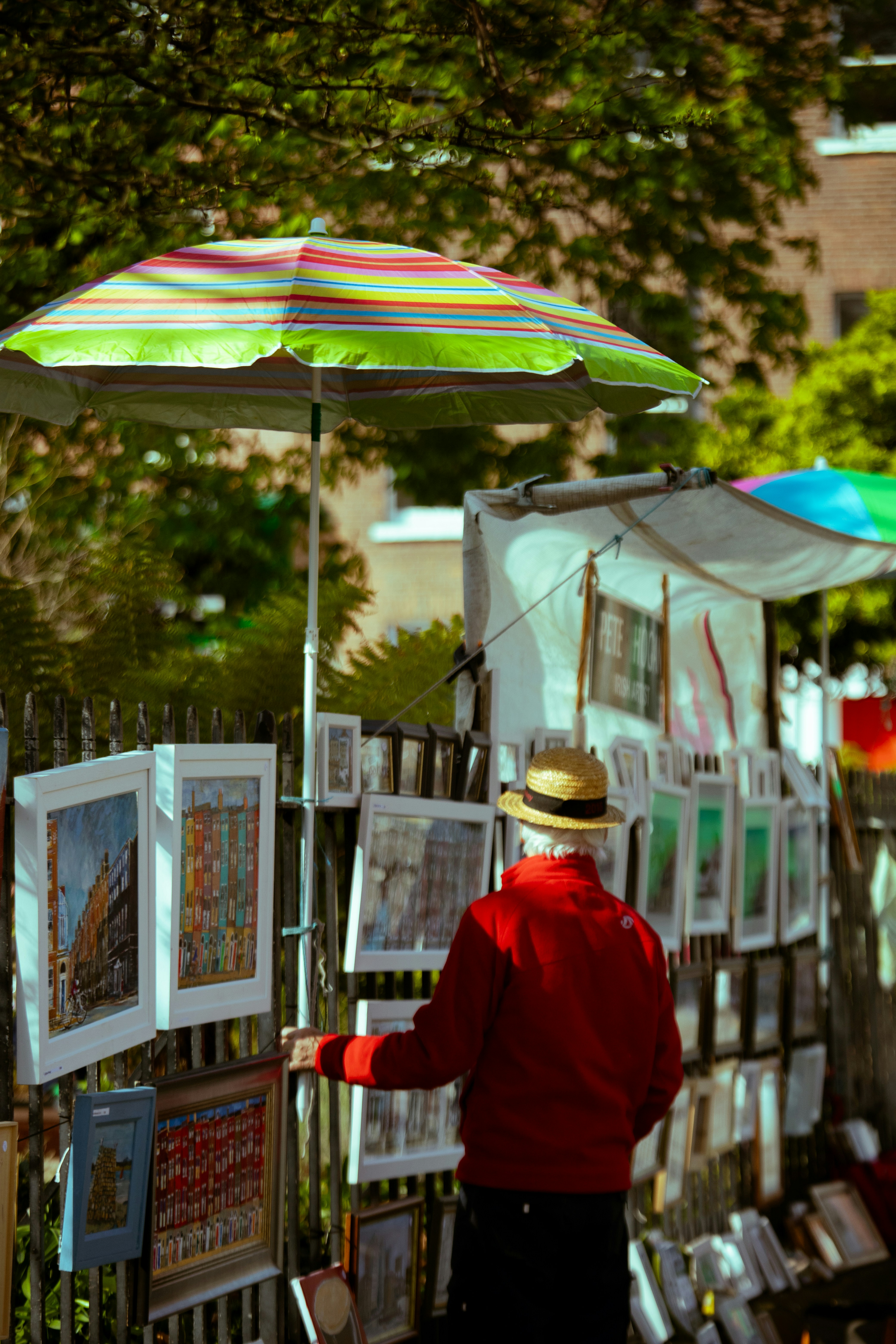 Red-clad Vendor at a Sunlit Art Market Under Colorful Umbrellas