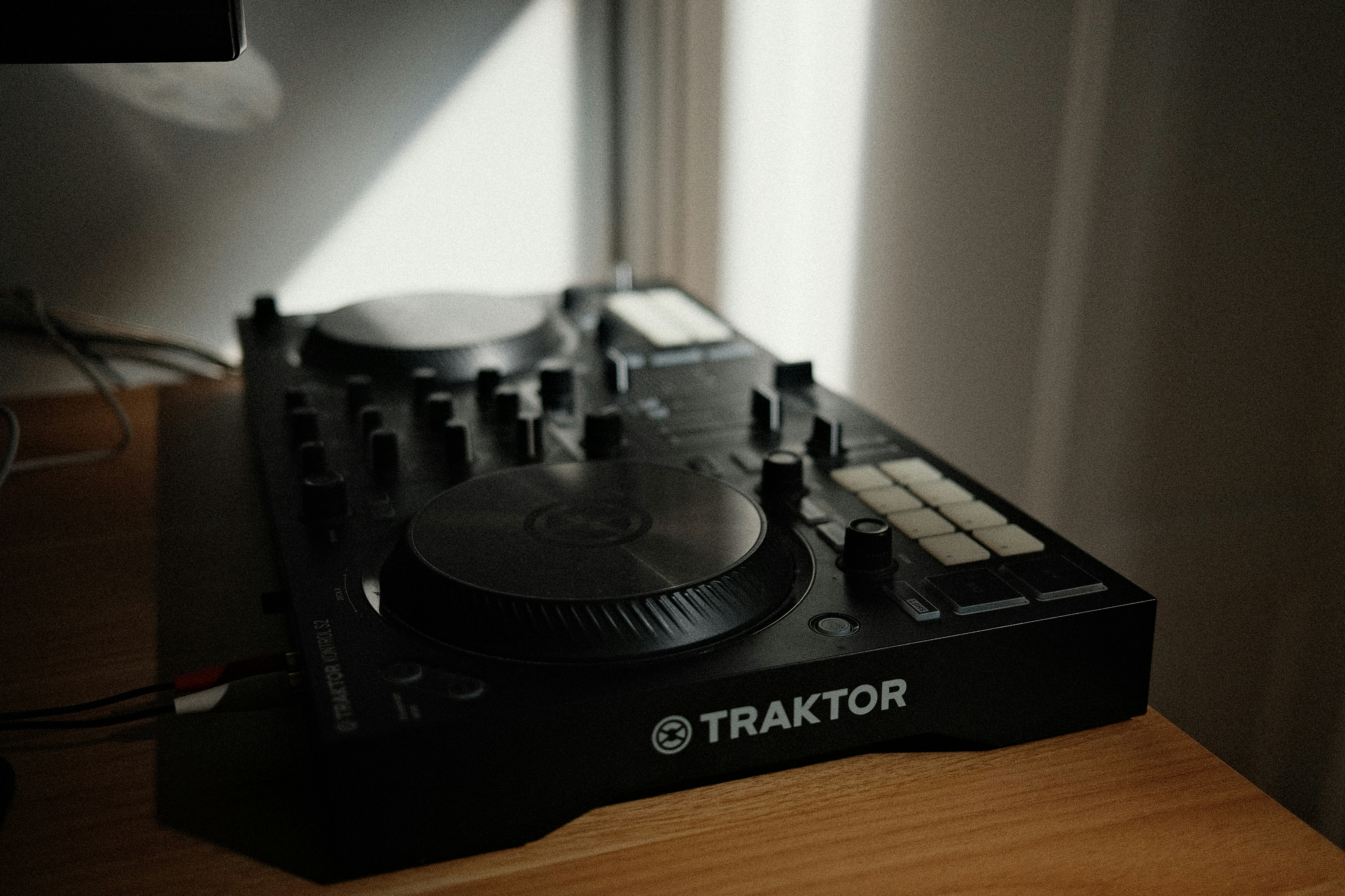 DJ controller resting on a wooden surface under indoor light, with subtle shadows and a moody tone; Traktor branding visible on the unit.