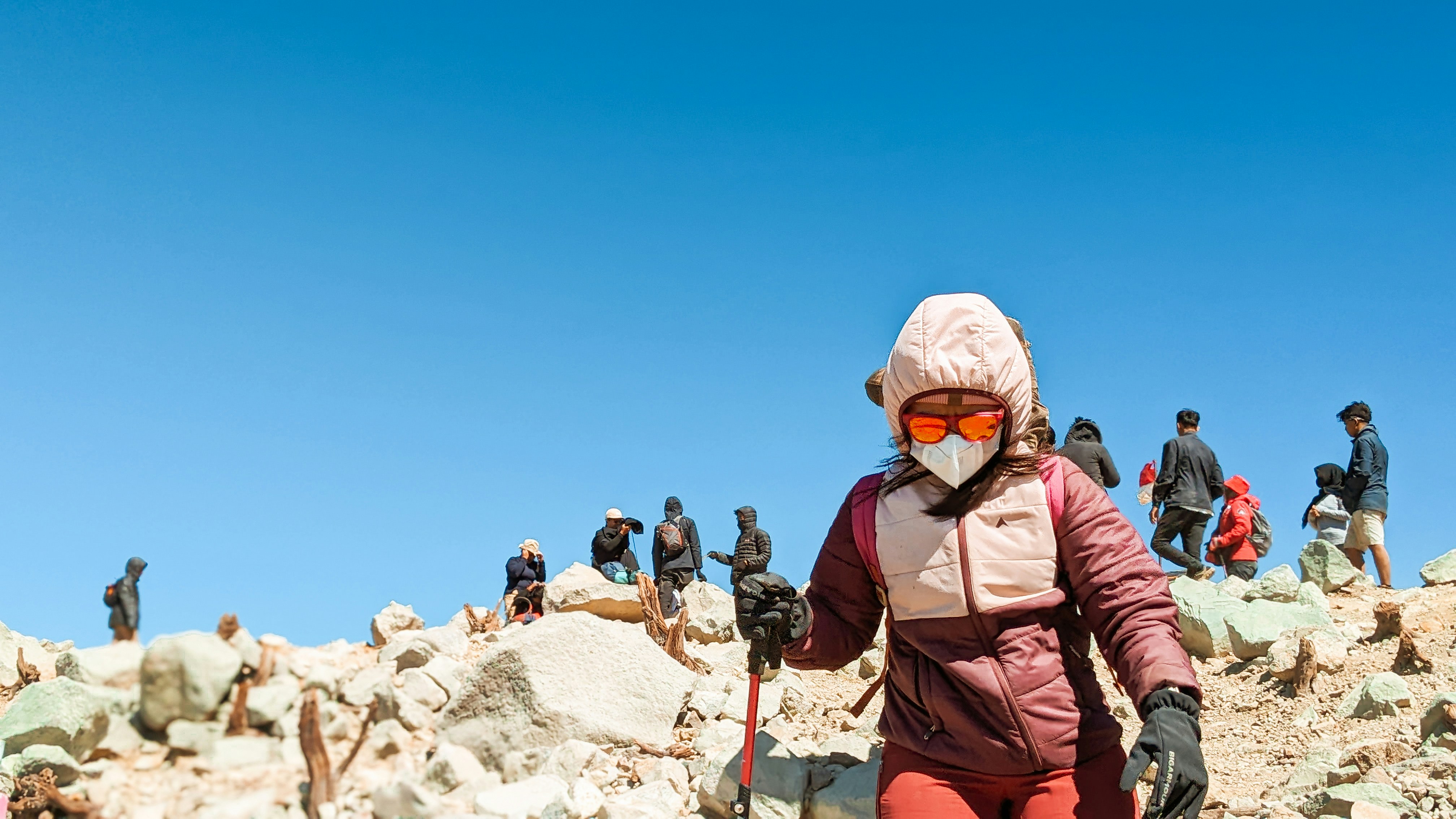 Climbing the sunlit ridge: hikers navigate rocky terrain under a clear blue sky