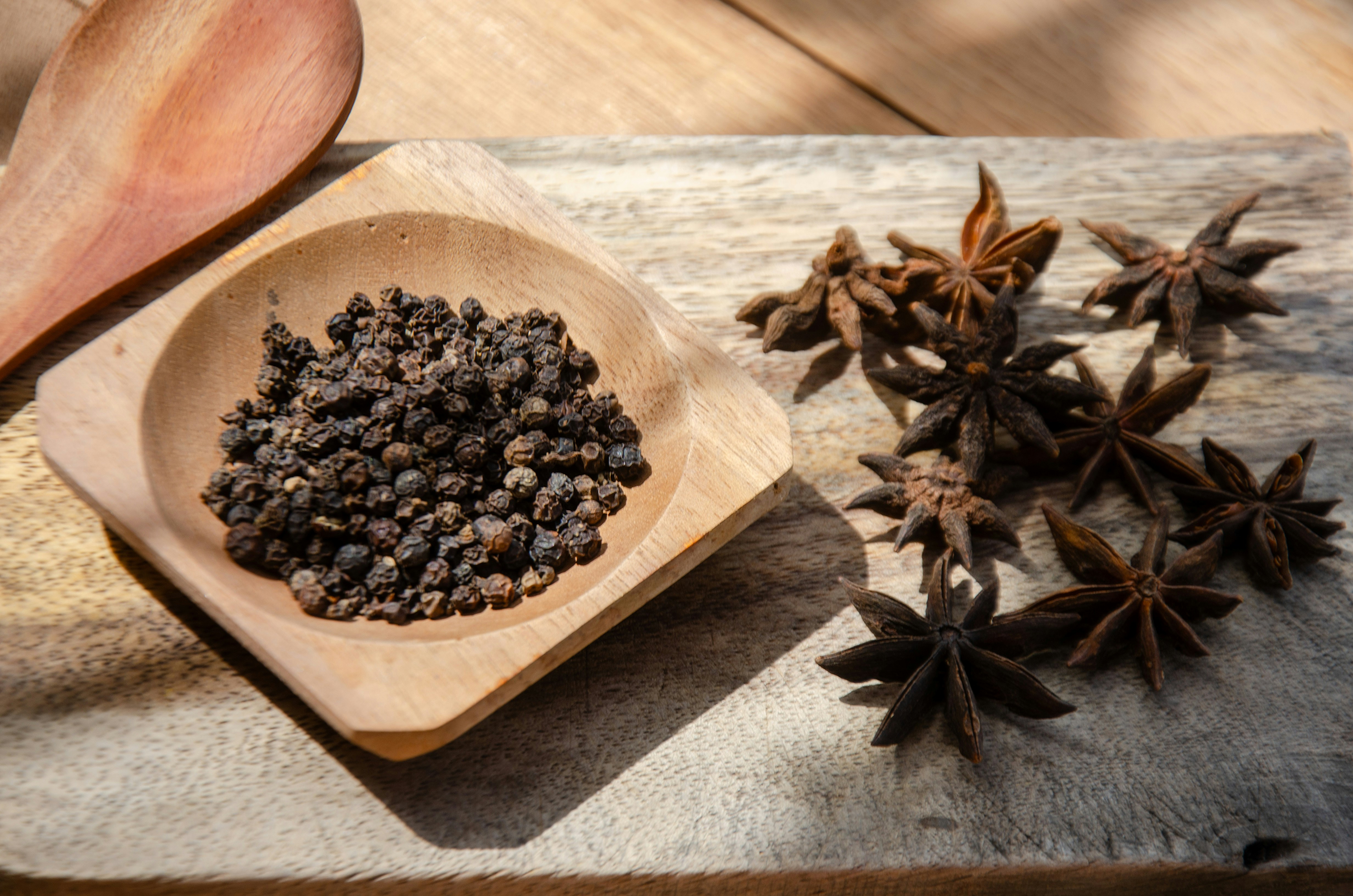 Black peppercorns in a wooden scoop with star anise on a rustic board