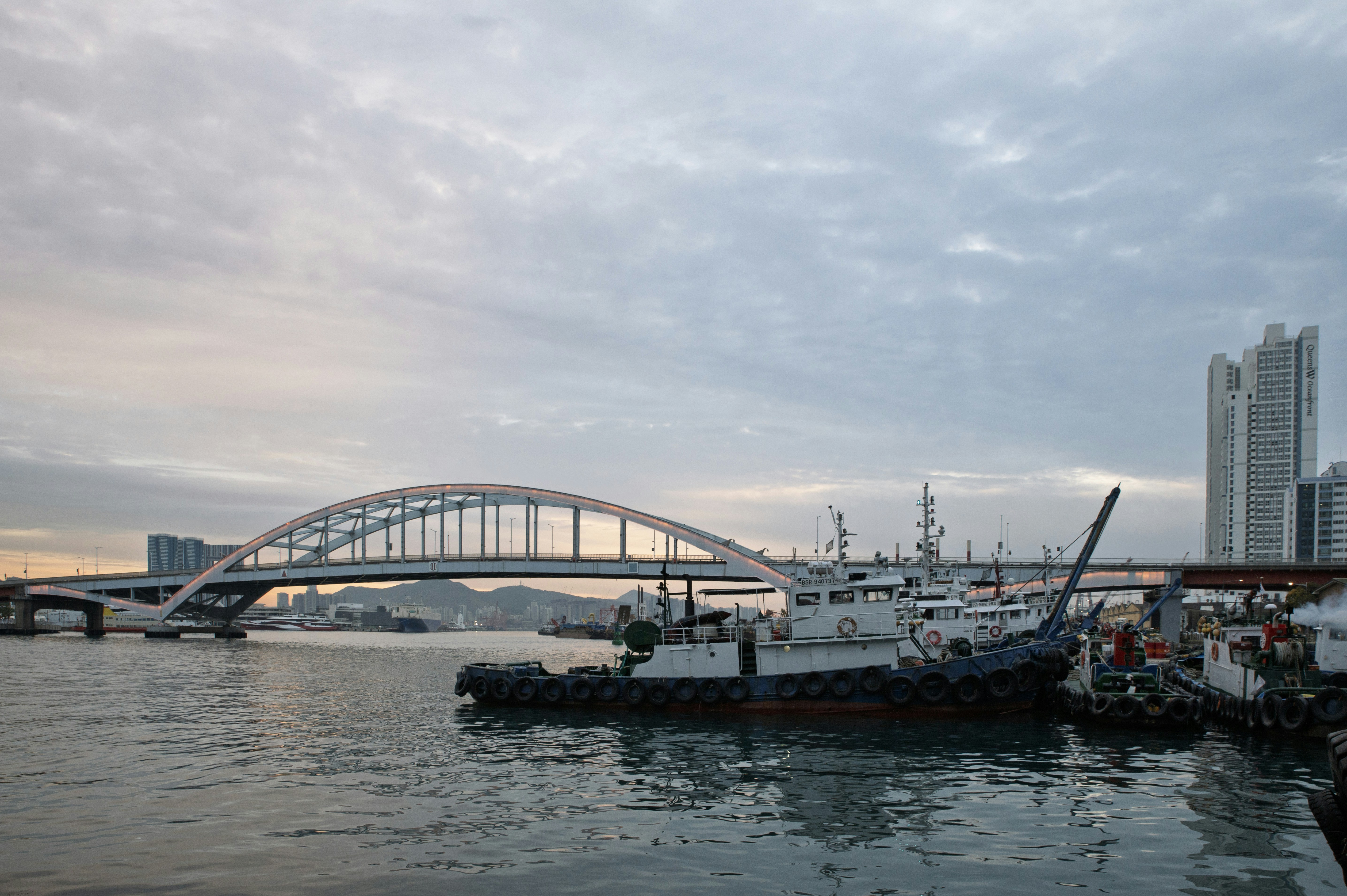 Towline at dusk: cranes, boats, and a curved bridge
